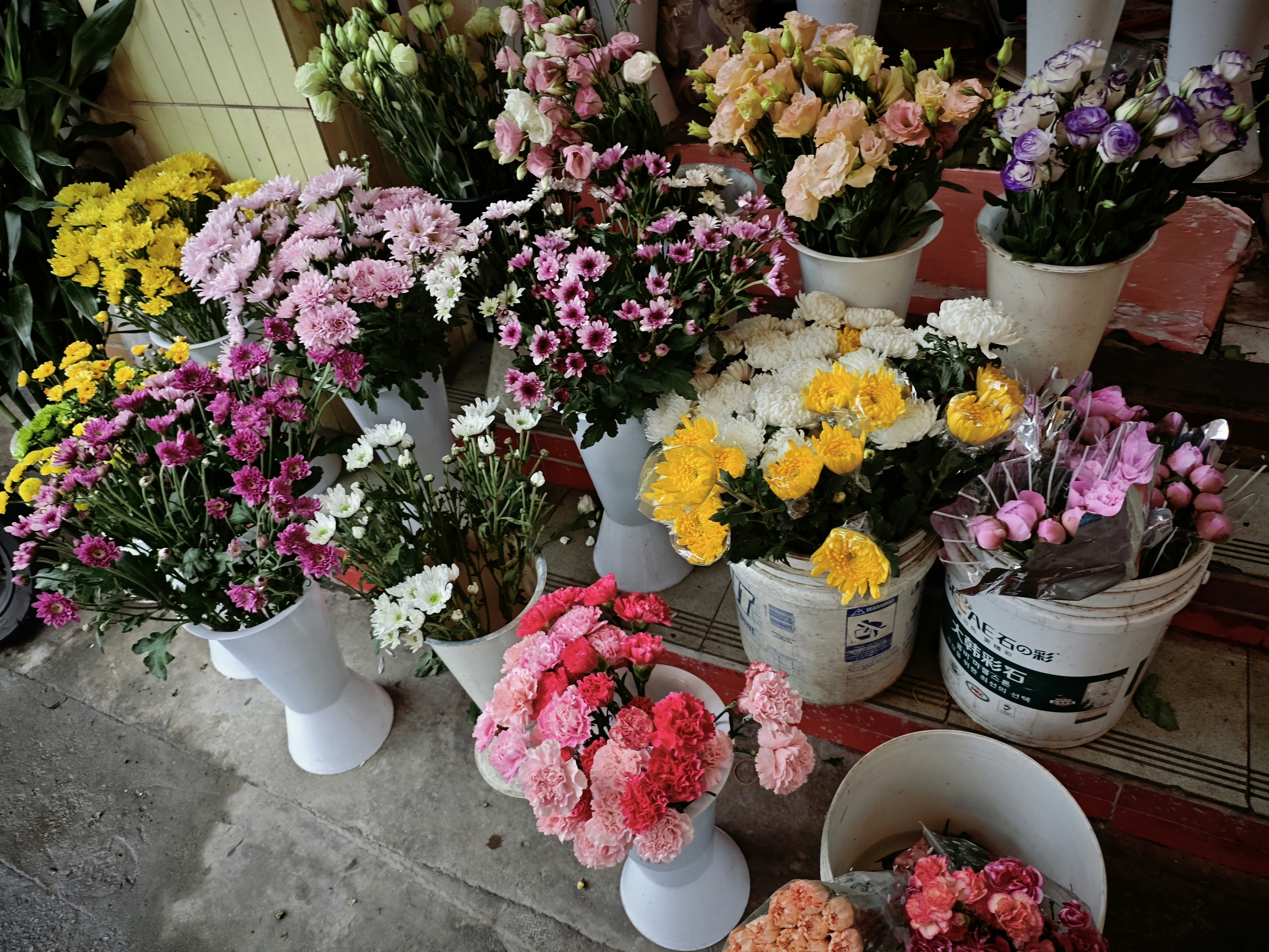 Buckets and vases filled with colorful chrysanthemums and carnations on a concrete floor