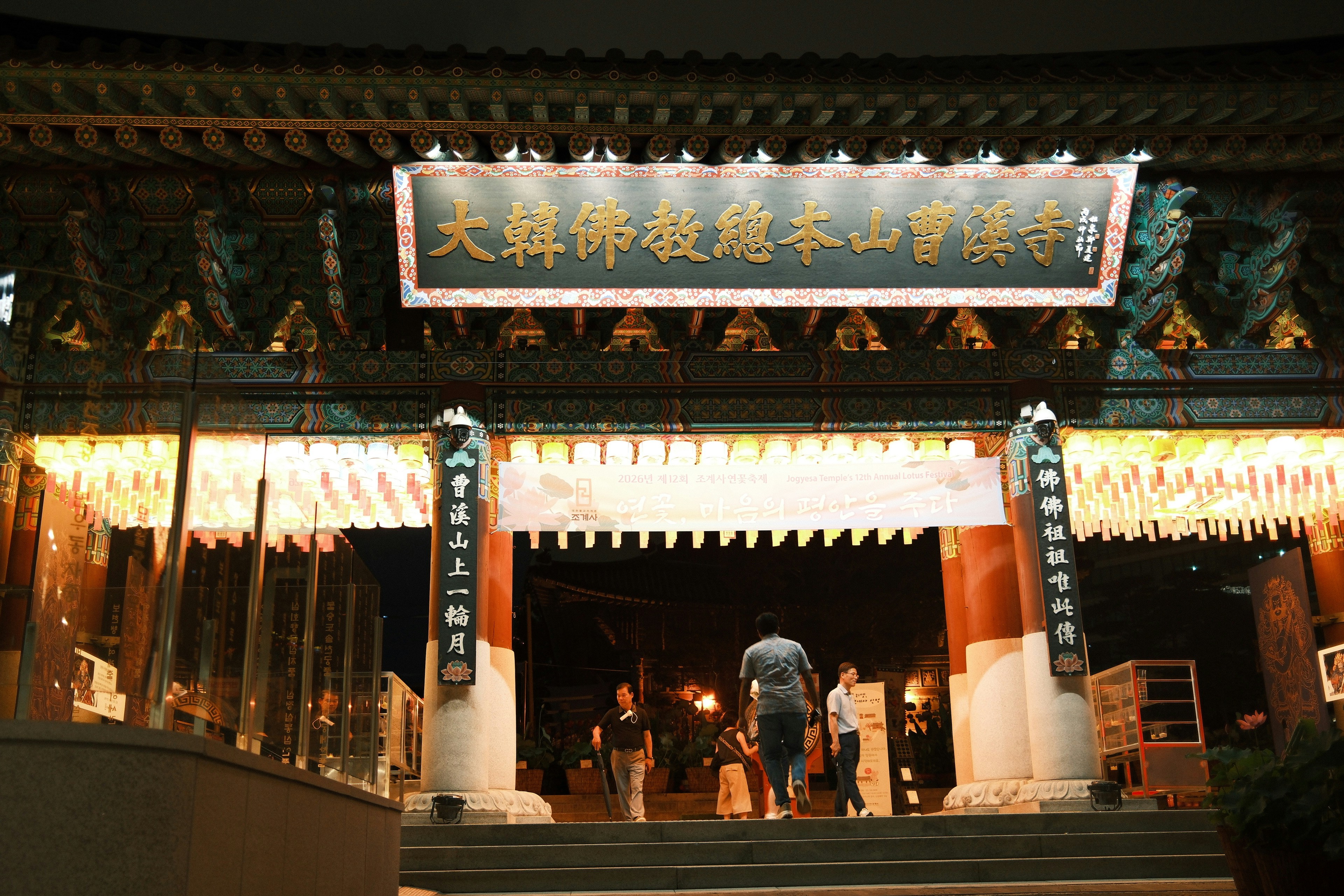 Night at the Lanterned Gate: People Enter a Korean temple under a gilded sign