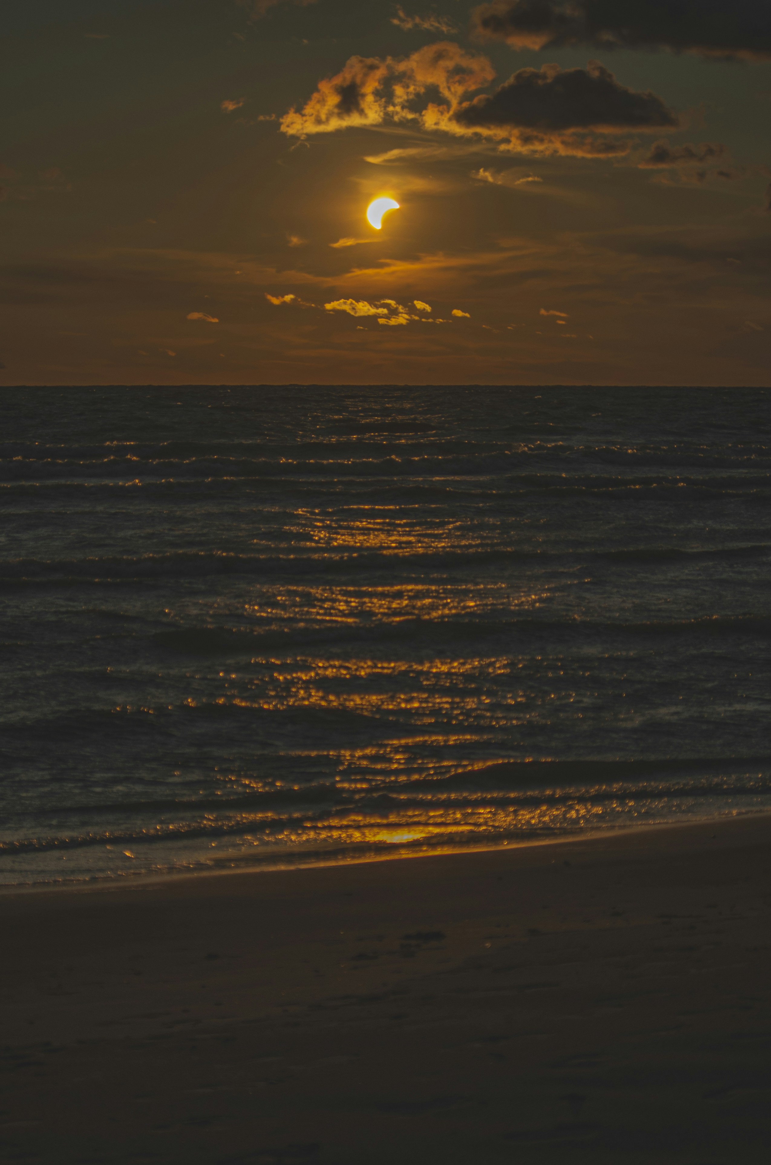 A partial solar eclipse over the ocean with golden light reflecting on waves