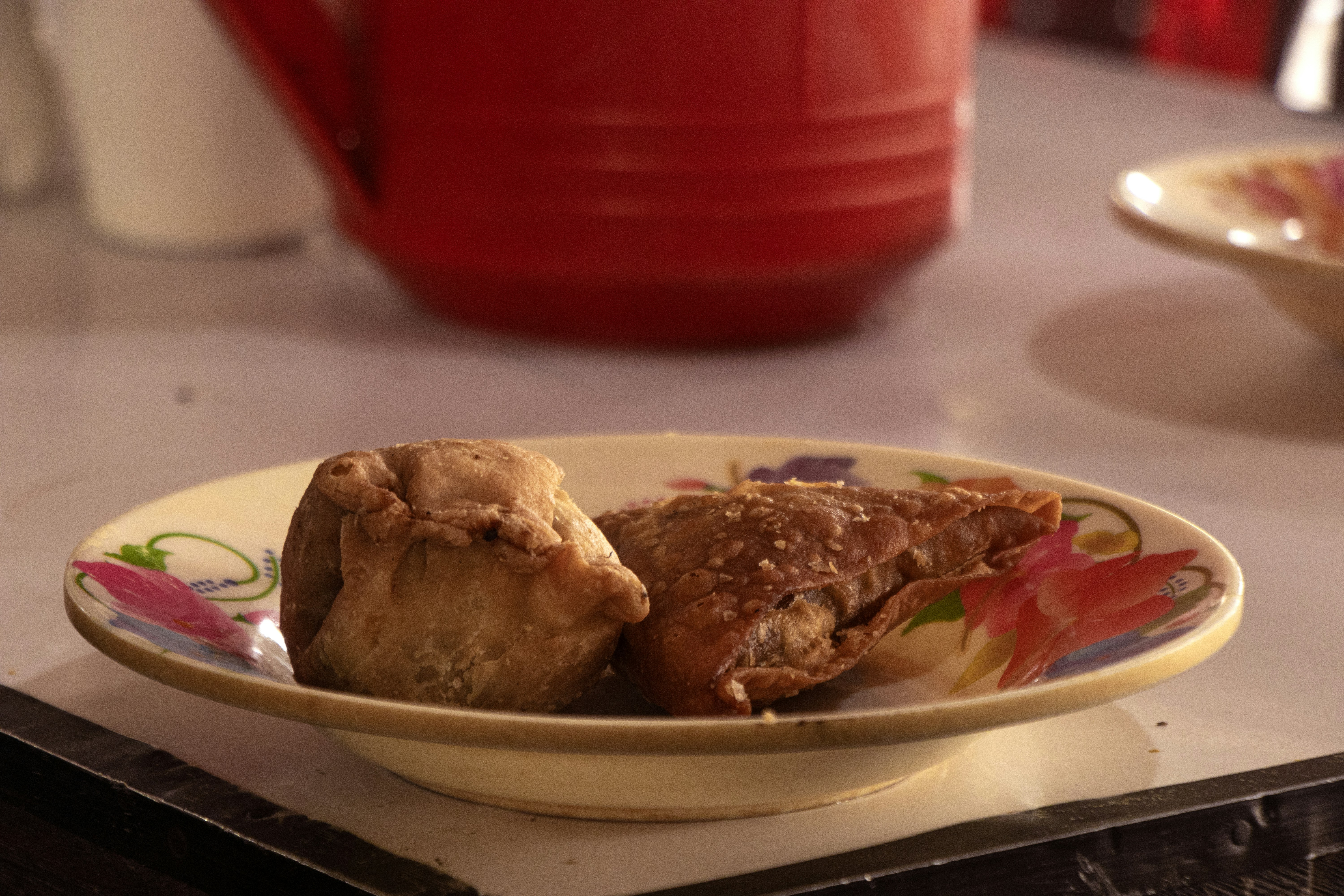 Two pastries rest on a floral plate on a kitchen counter, with a red pitcher and other dishware in the background.