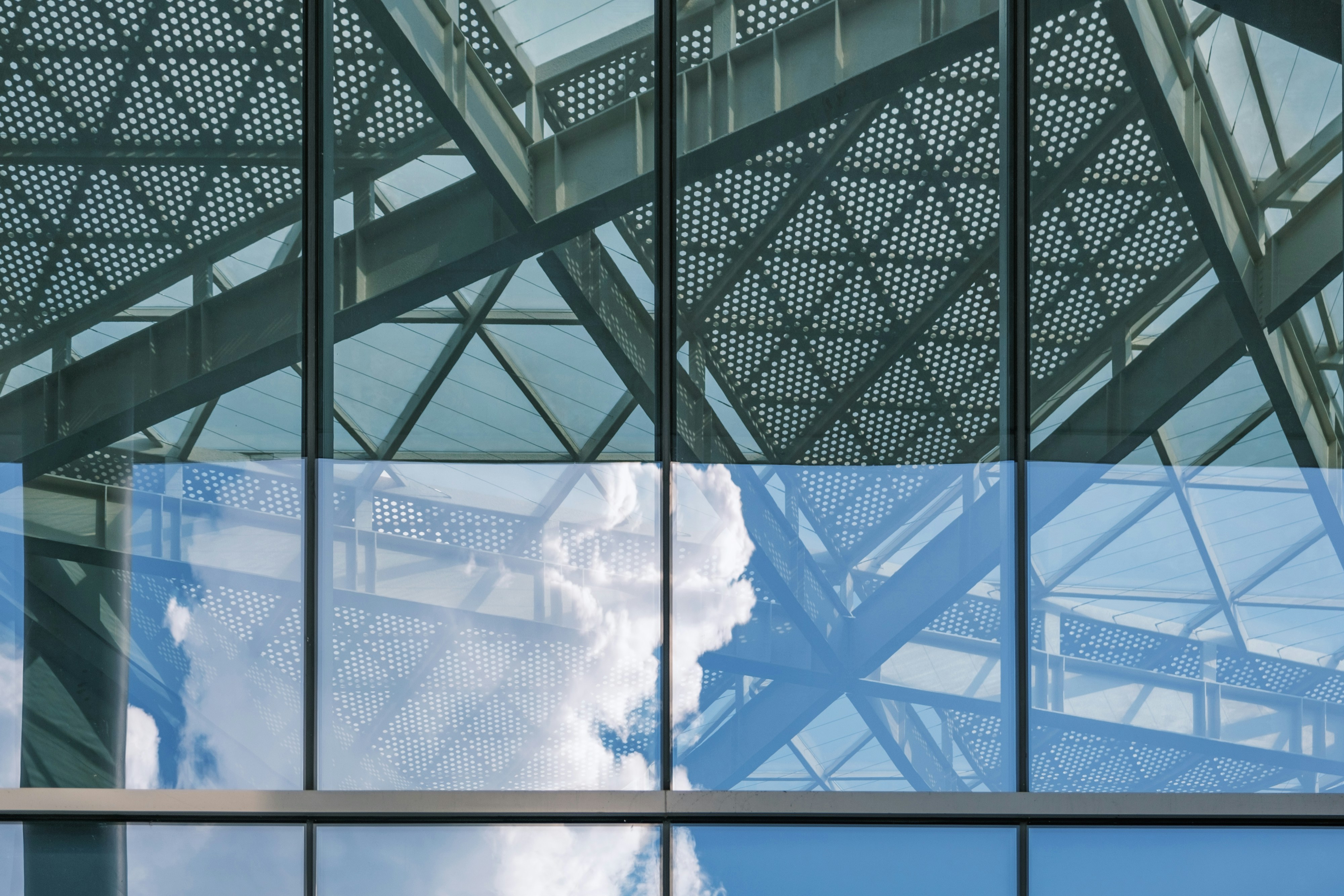 Glass facade with metal lattice and reflected sky, highlighting architectural geometry and blue-tinted panels.