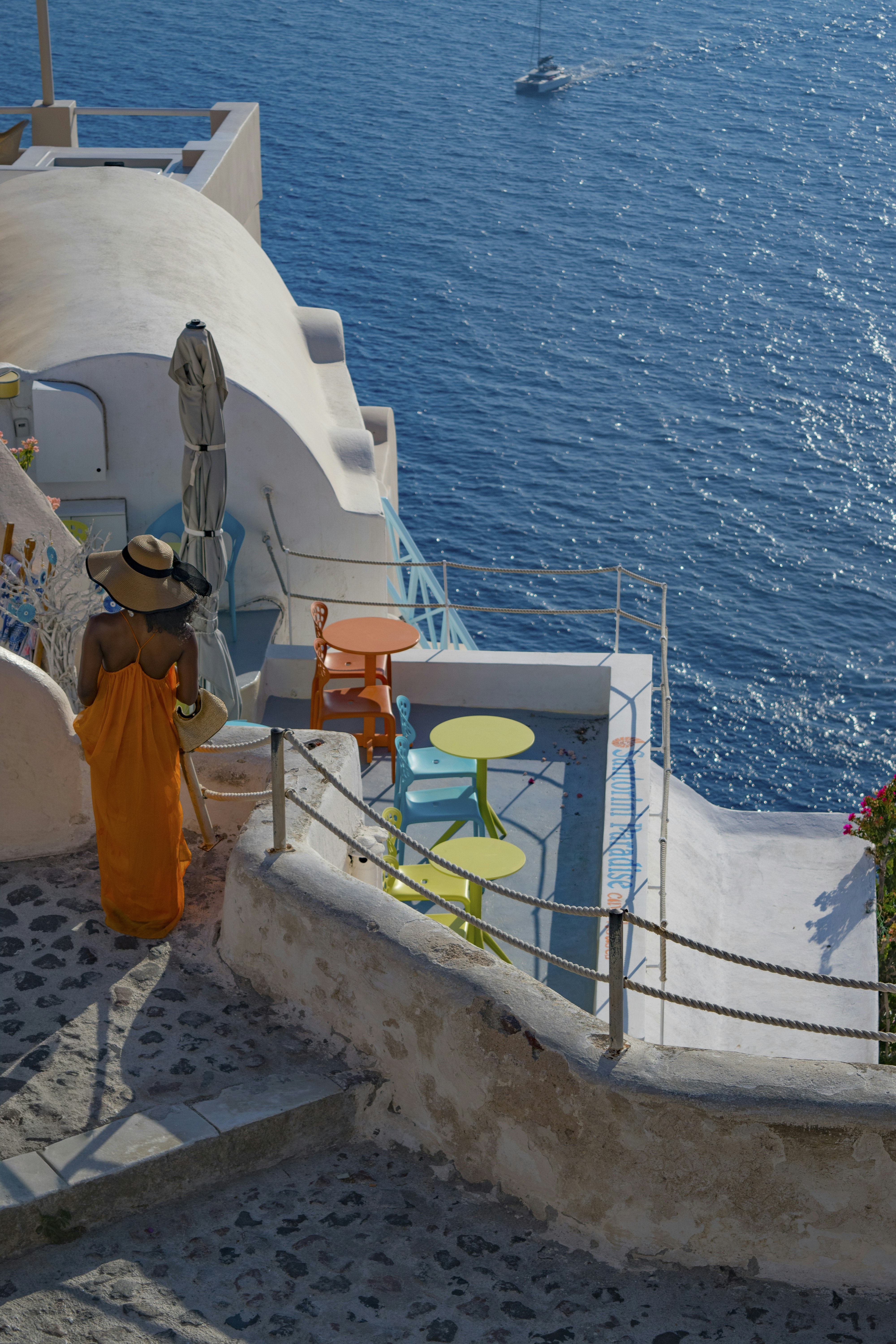 Sunlit Terrace Over the Aegean: A Woman in Orange at the Cliffside Steps