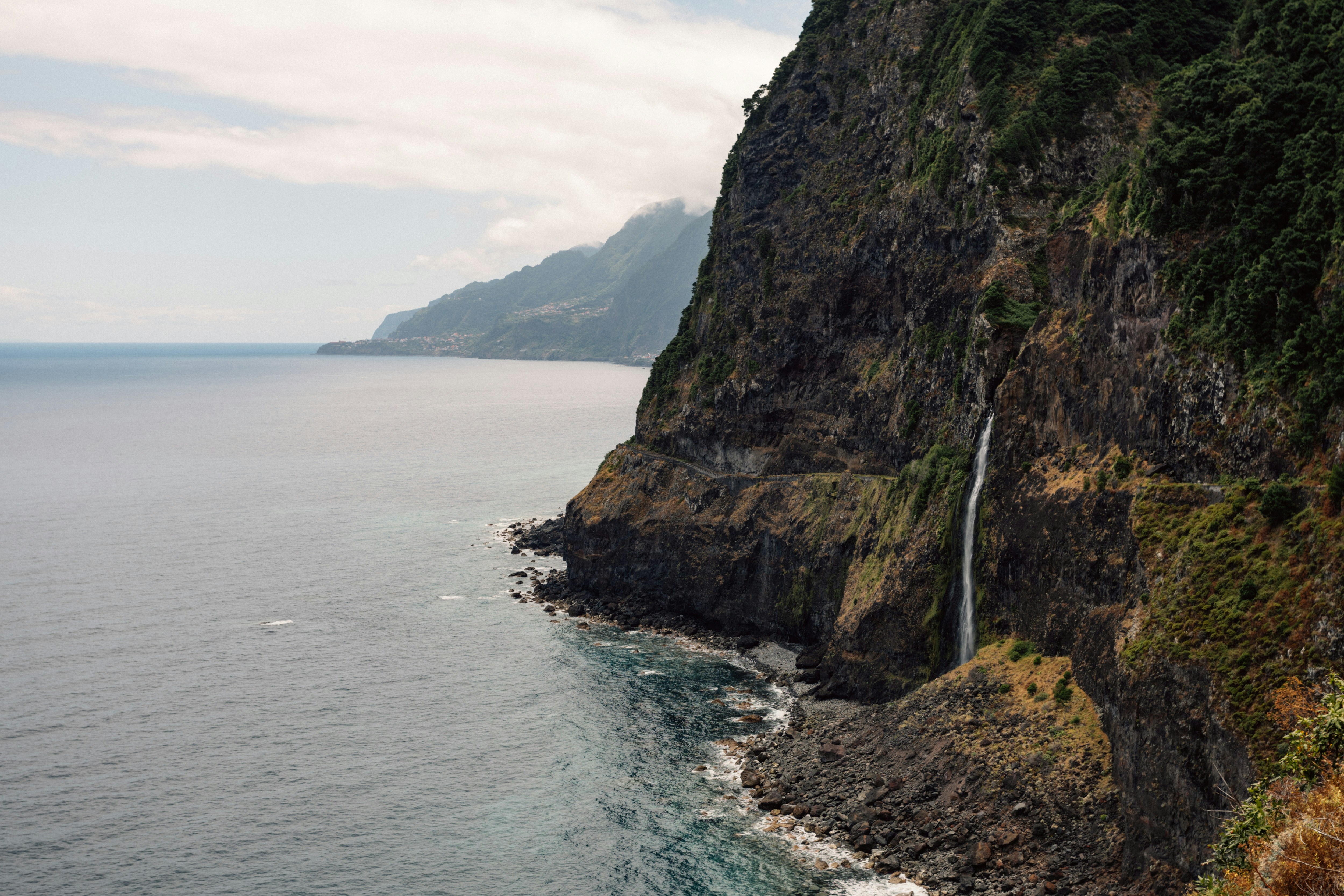 Cliff-edge Cascade: A Narrow Vista of Sea and Veiled Waterfall