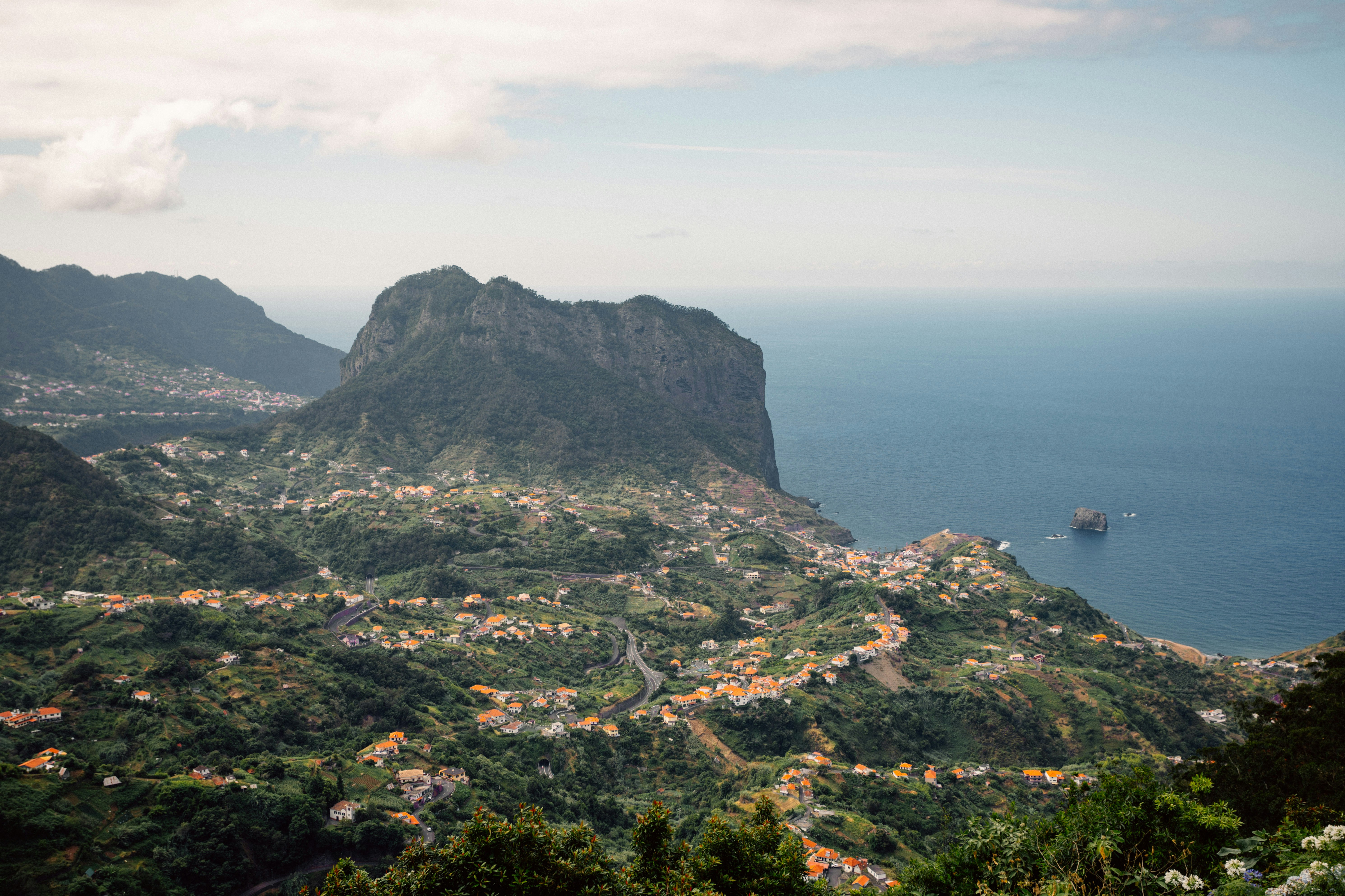 A coastal village with orange roofs nestled in green mountains above the ocean.
