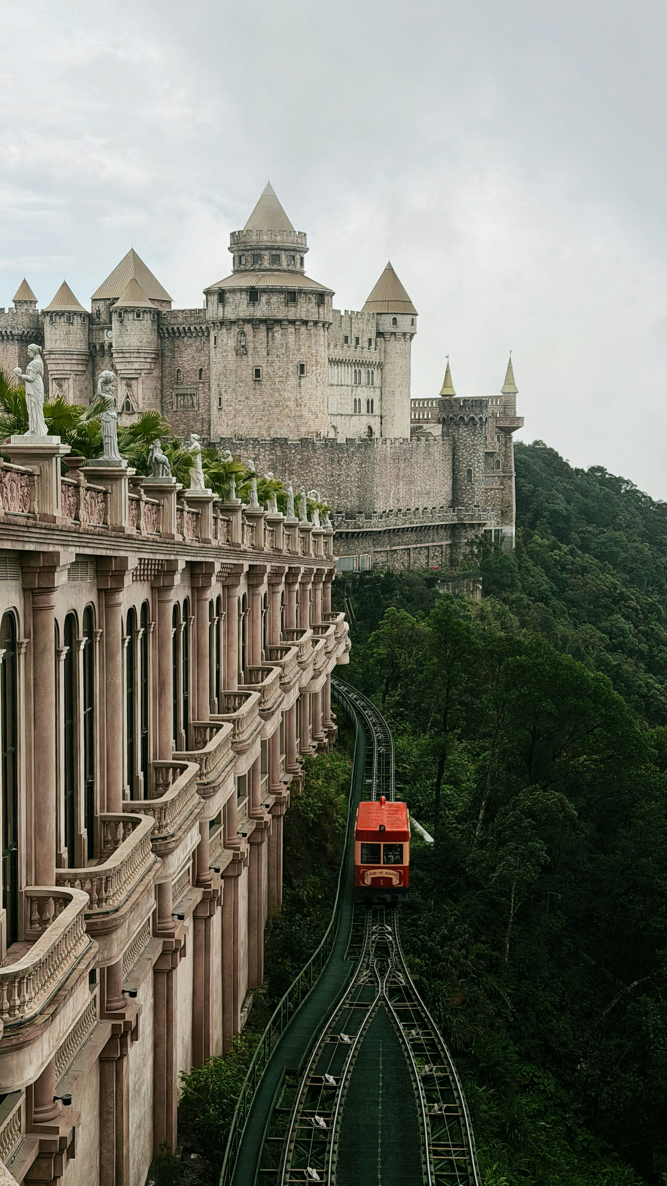 Red funicular climbing through the French Village at Ba Na Hills, Da Nang, Vietnam, with European-inspired castle architecture overlooking the forested mountains.