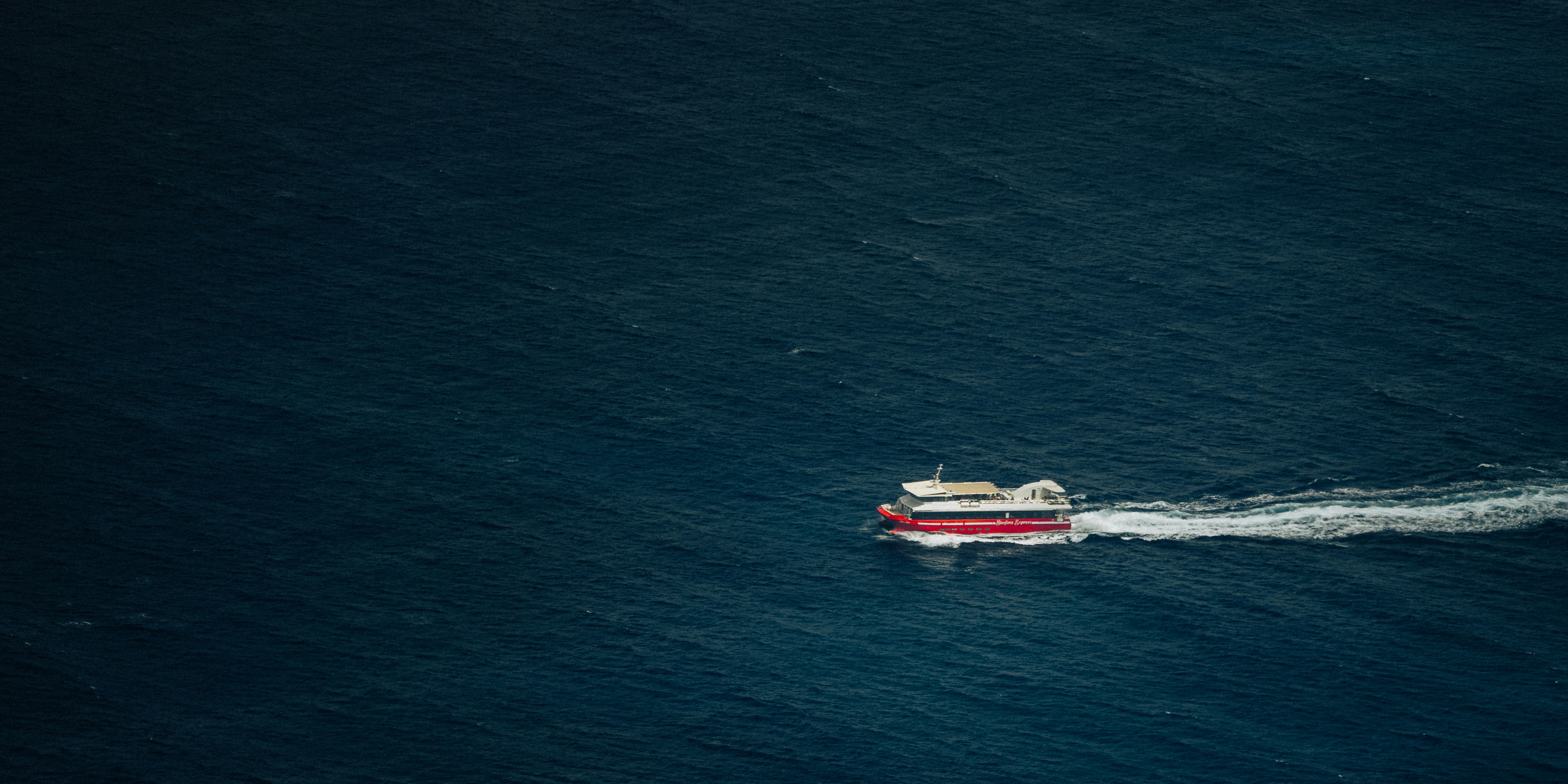 Red and white passenger boat carving a white wake across a blue ocean