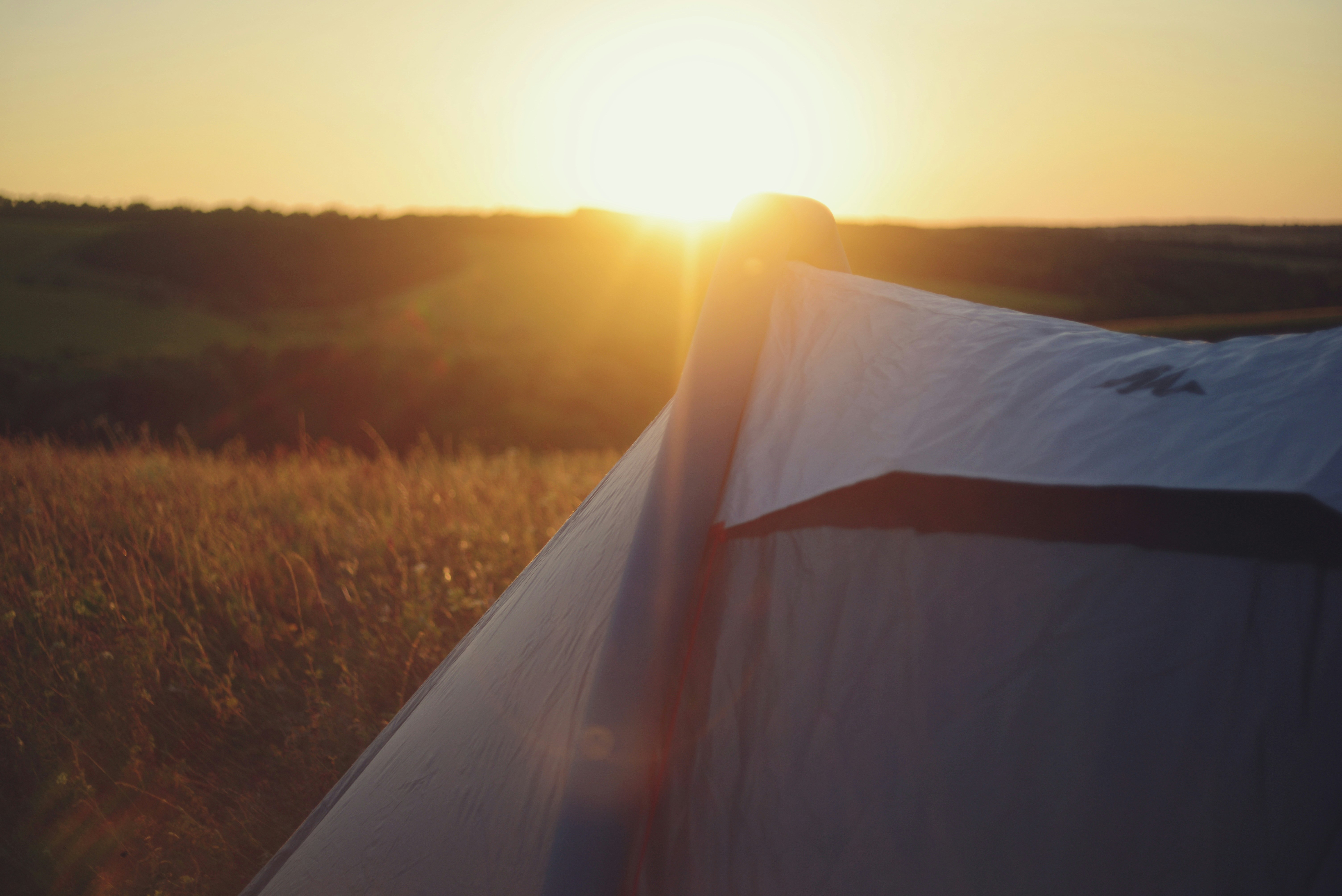 A white tent in a grassy field during the golden hour.