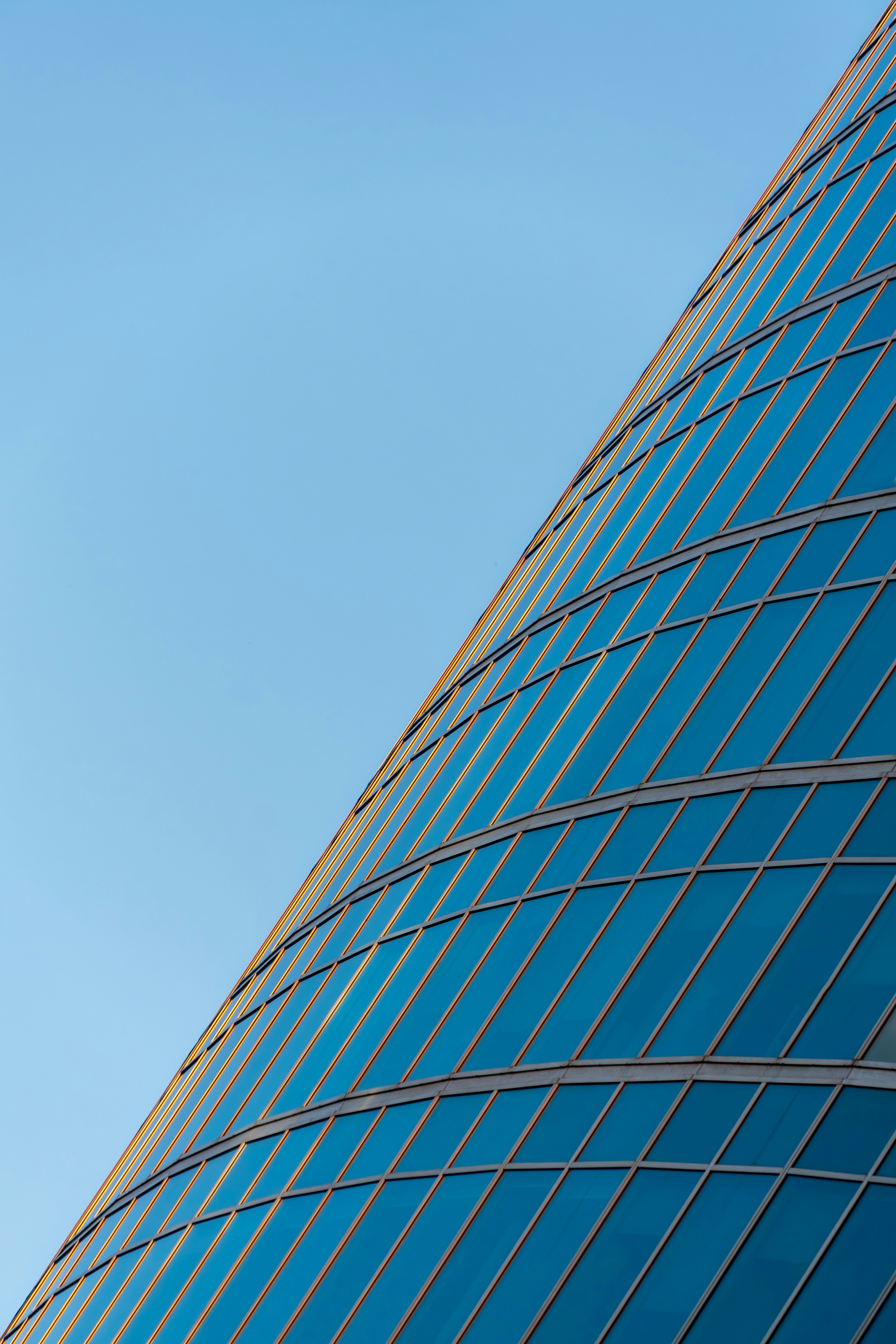 Blue-tinted glass panels curve across a high-rise facade, catching warm sunlight along the edges and reflecting a clear sky.
