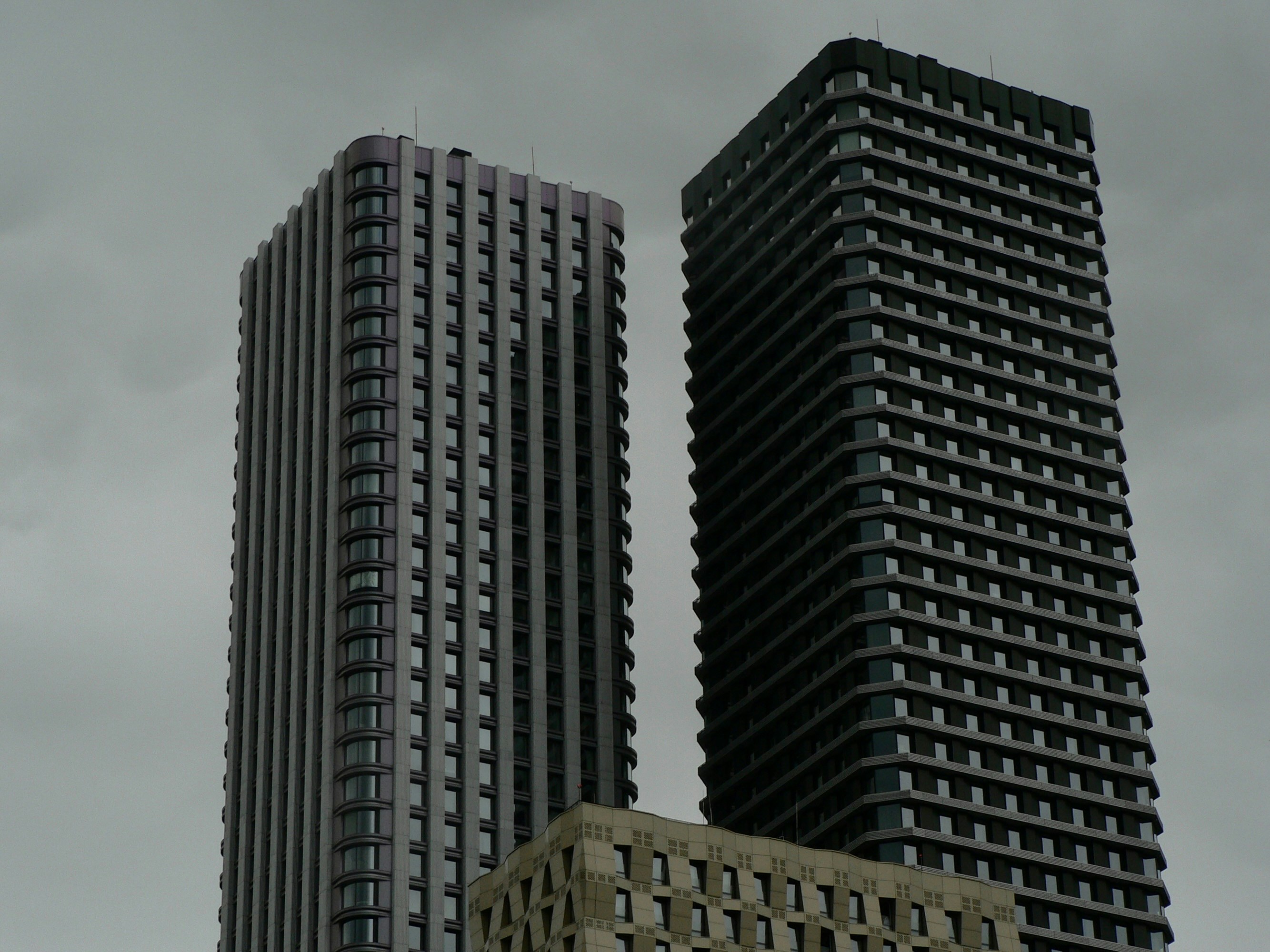 A close‑up view of soaring skyscrapers against a cold, gloomy grey sky. The overcast weather and moody lighting create a dramatic, melancholic urban atmosphere, captured with a Panasonic Lumix DMC‑FZ5.