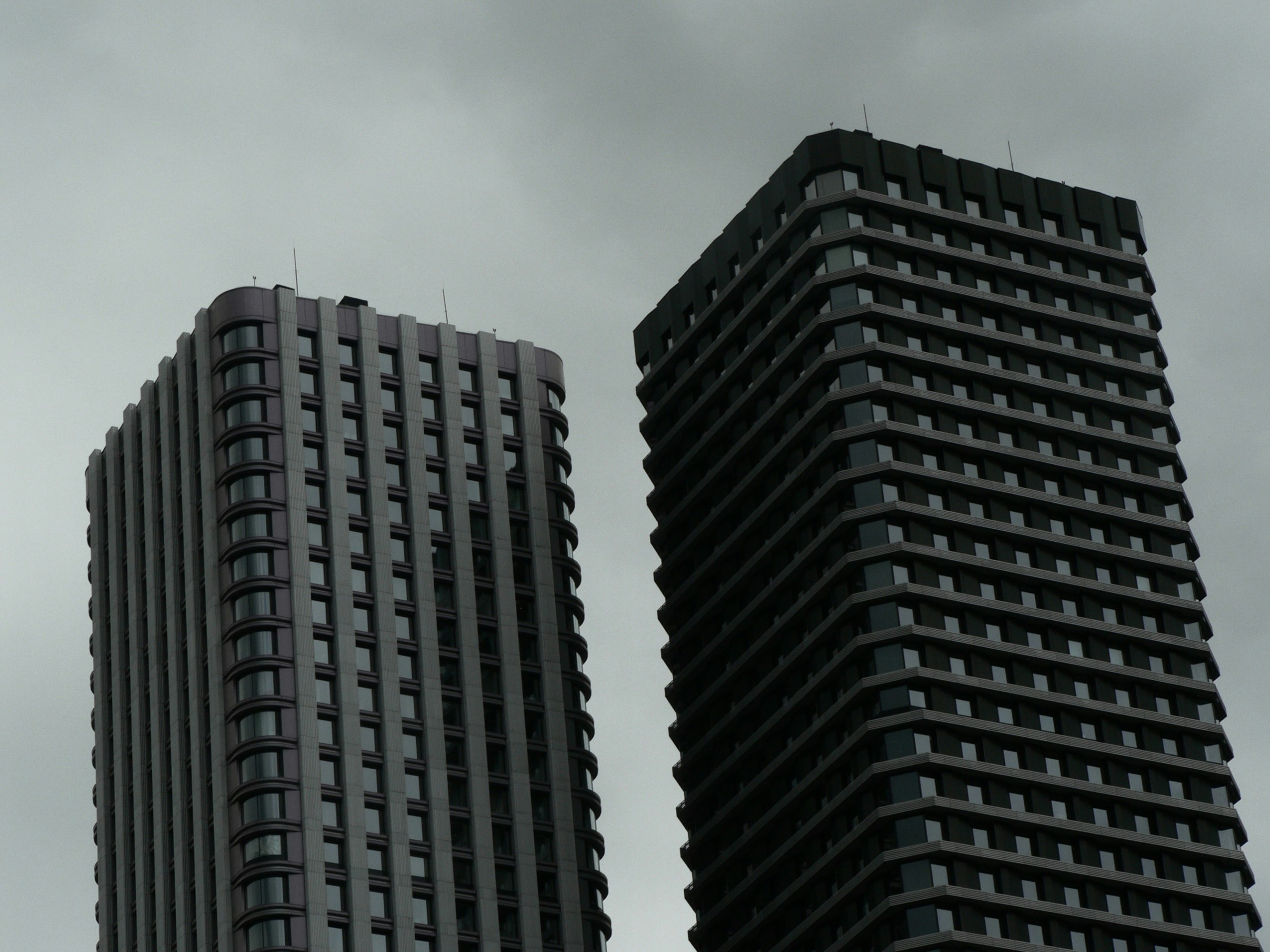A close‑up view of soaring skyscrapers against a cold, gloomy grey sky. The overcast weather and moody lighting create a dramatic, melancholic urban atmosphere, captured with a Panasonic Lumix DMC‑FZ5.