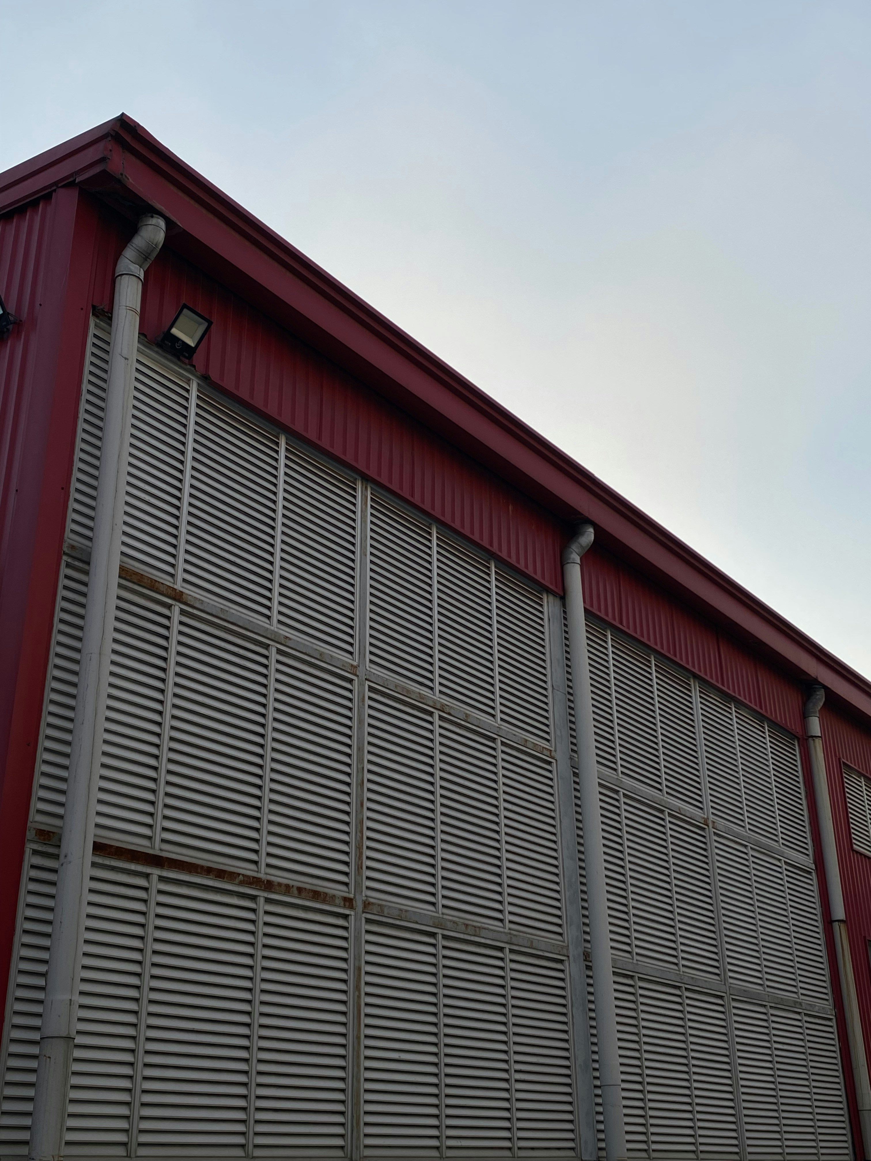 Close-up of a red-equipped industrial wall with grey vent panels and vertical pipes, emphasizing the building's utilitarian facade.
