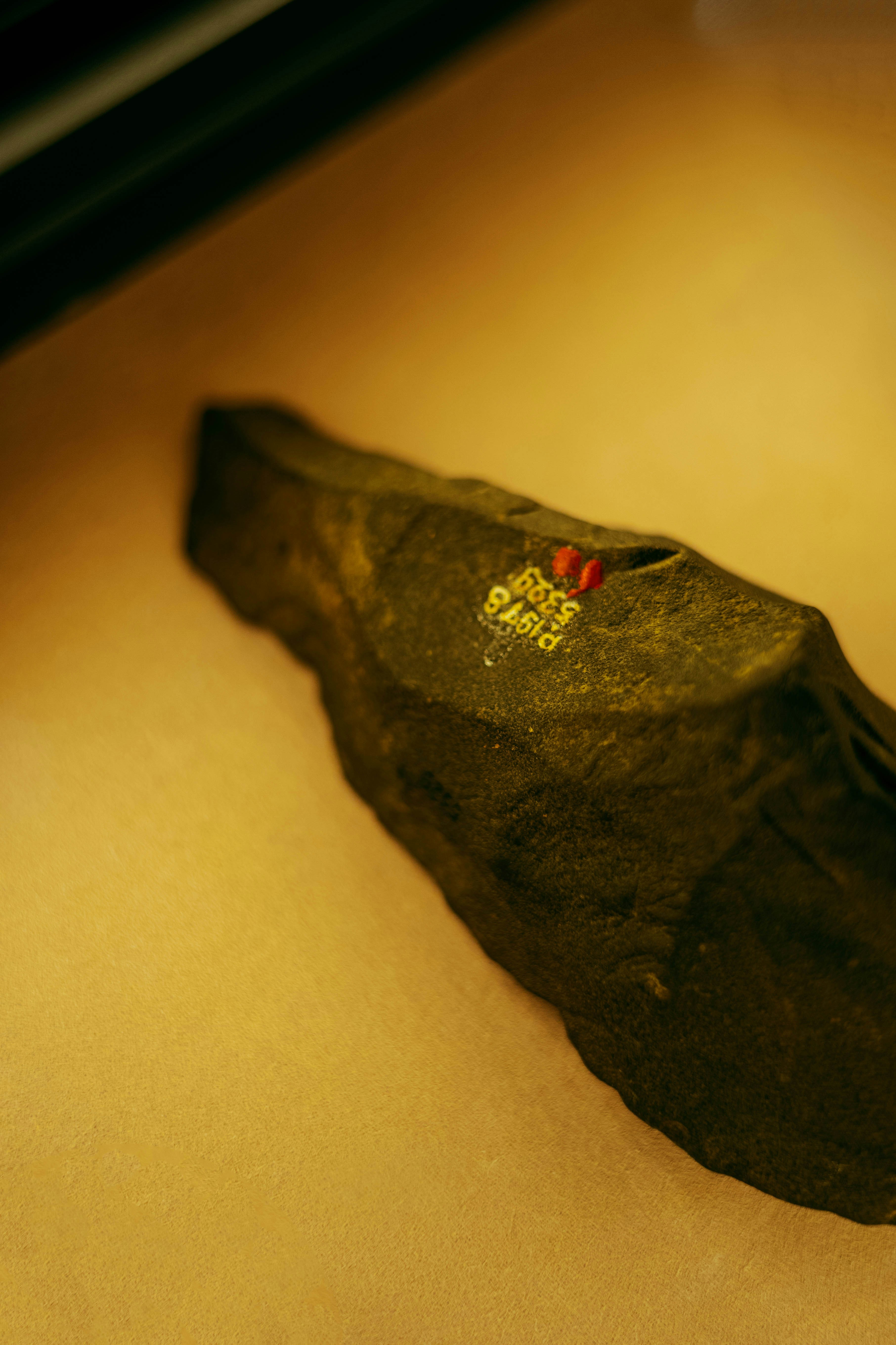 Small red-marked rock fragment under warm light on a sandy surface