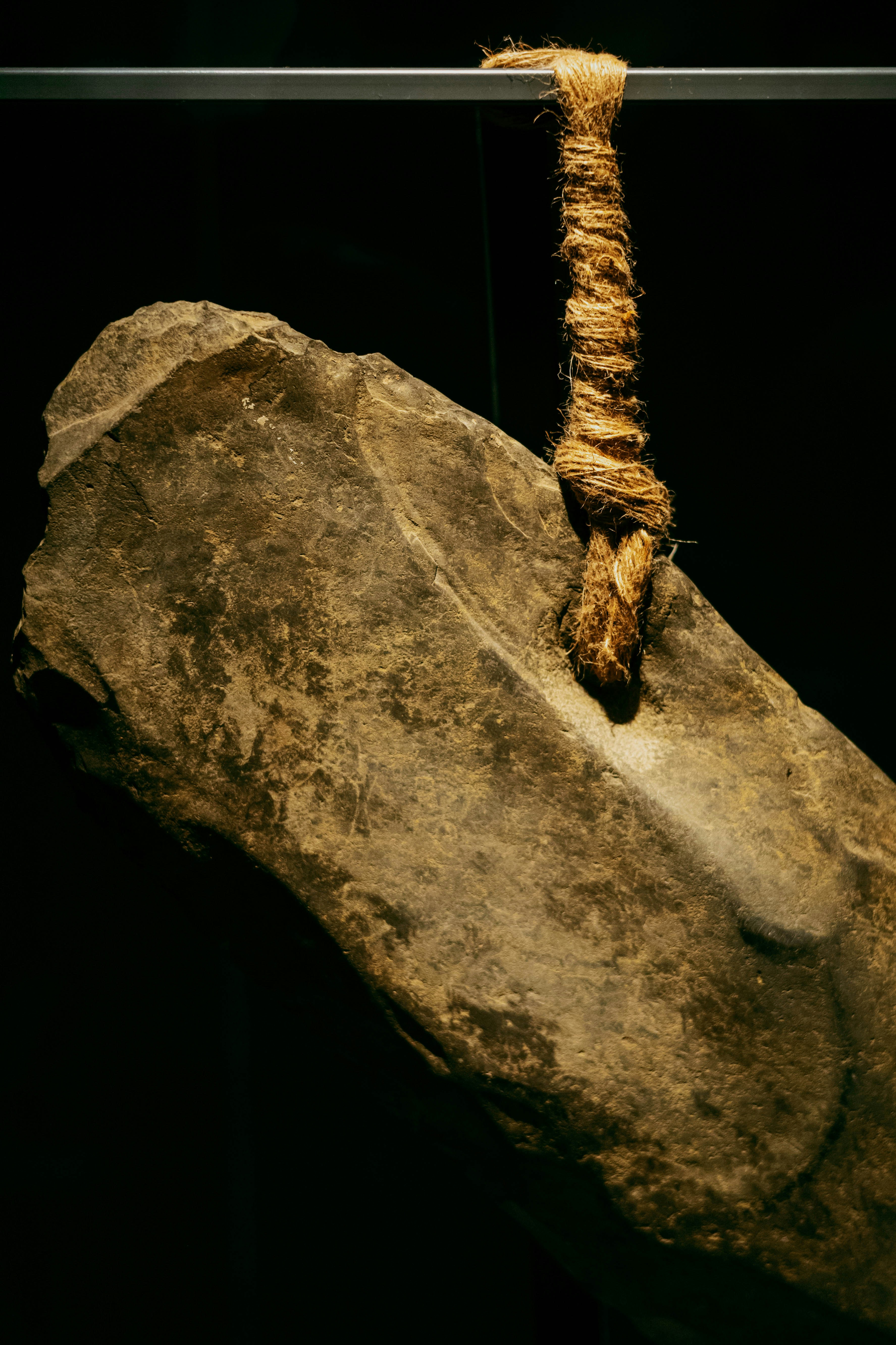 Rope and Stone: A Weathered Anchor Suspended Over Quiet Darkness