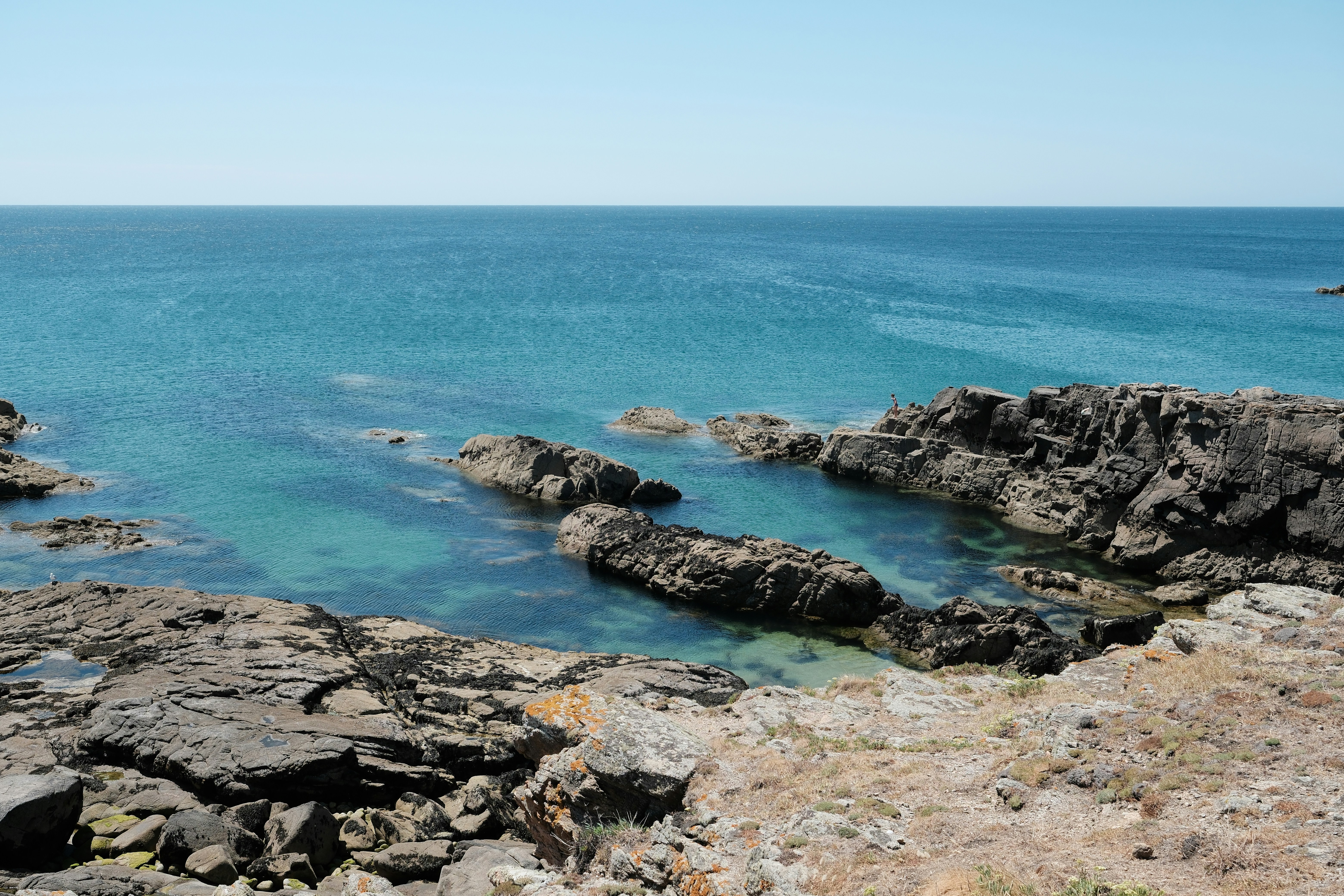 Sunlit Tide: Rugged Rocks Meet Clear Aquamarine Waters