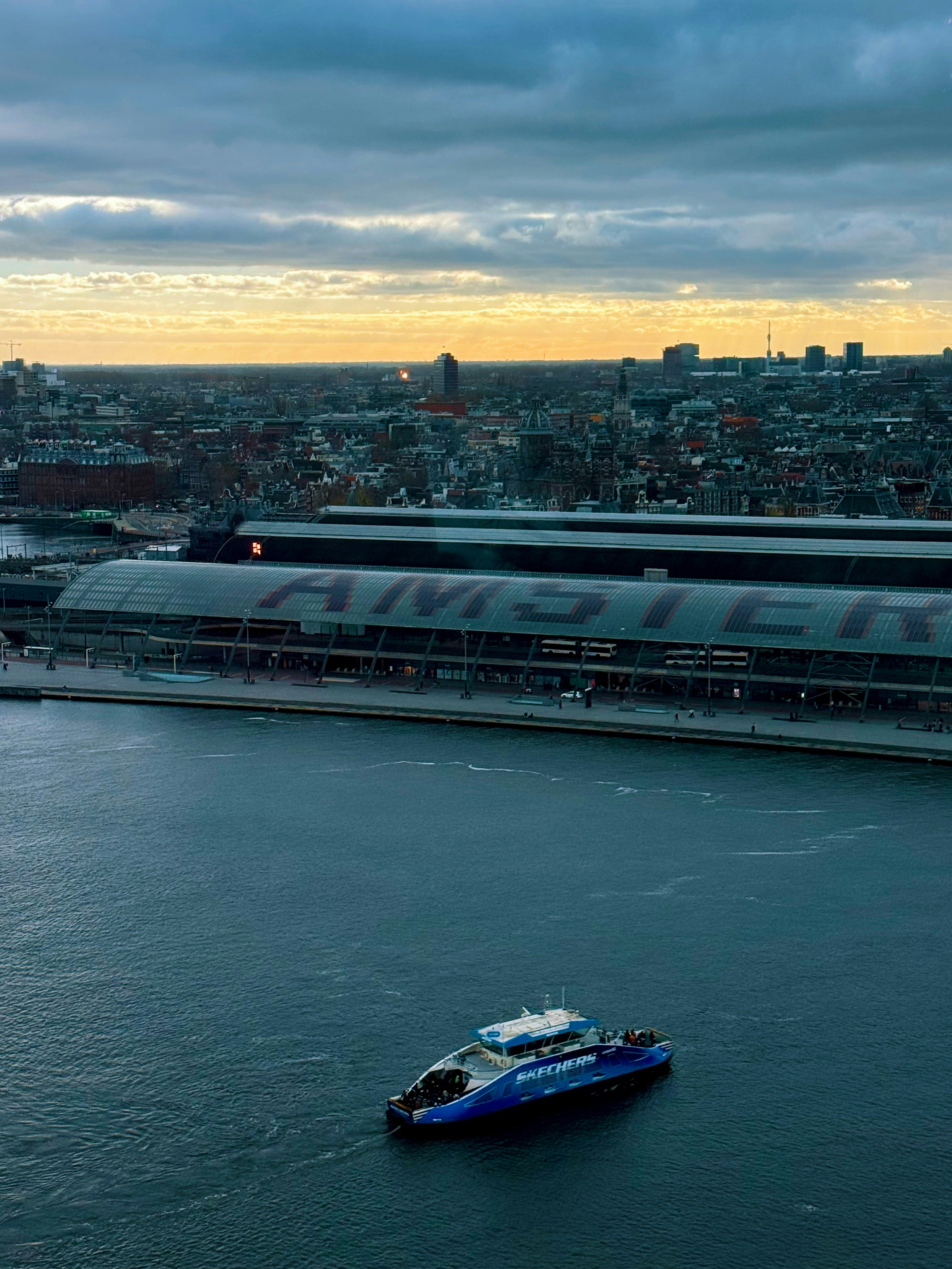 Harbor Wake: A Blue Ferry Across the Thames-esque River Against a Distant City Horizon