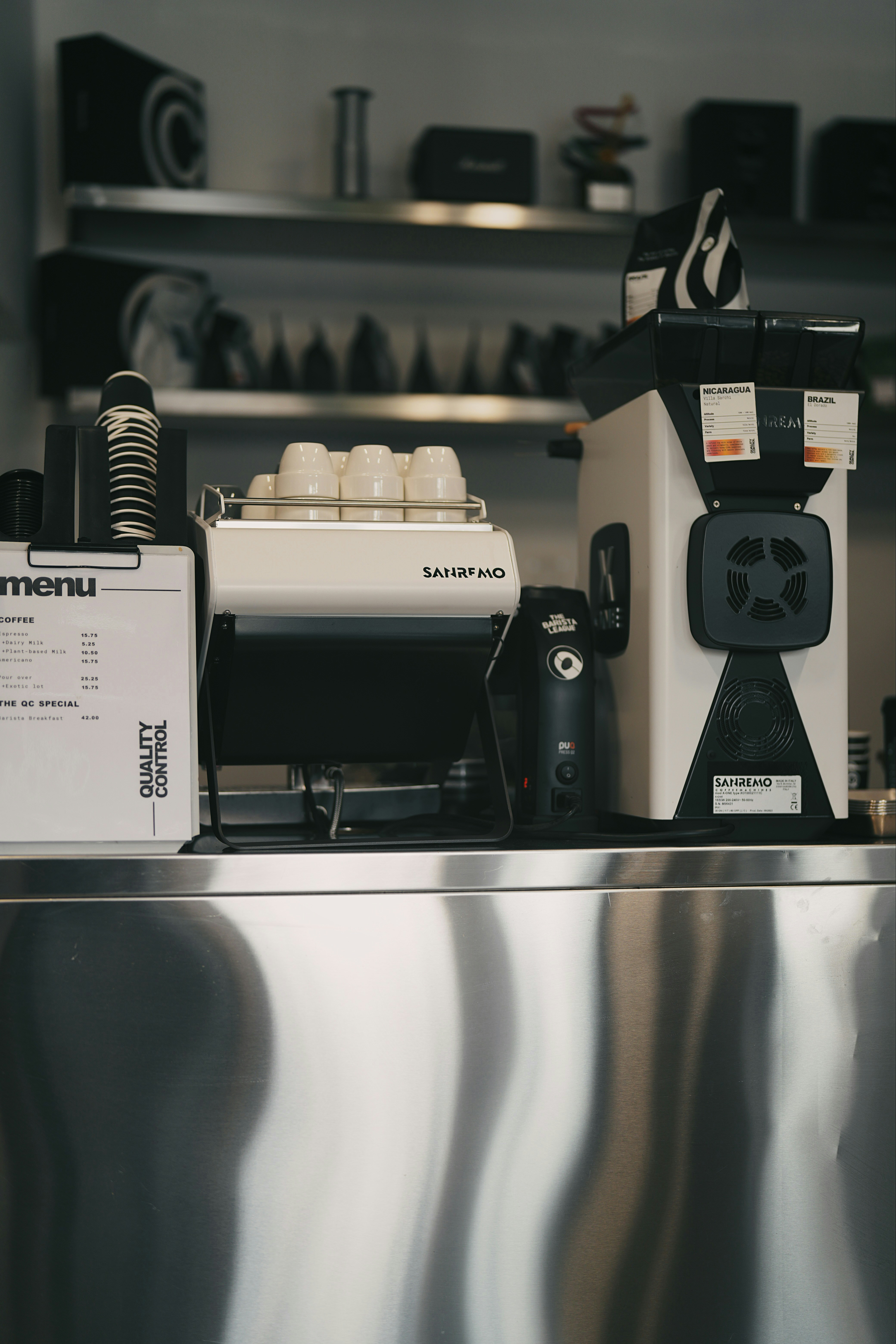 Sleek coffee station featuring a compact espresso machine and a high-capacity grinder on a stainless steel counter, hinting at a professional cafe setup.