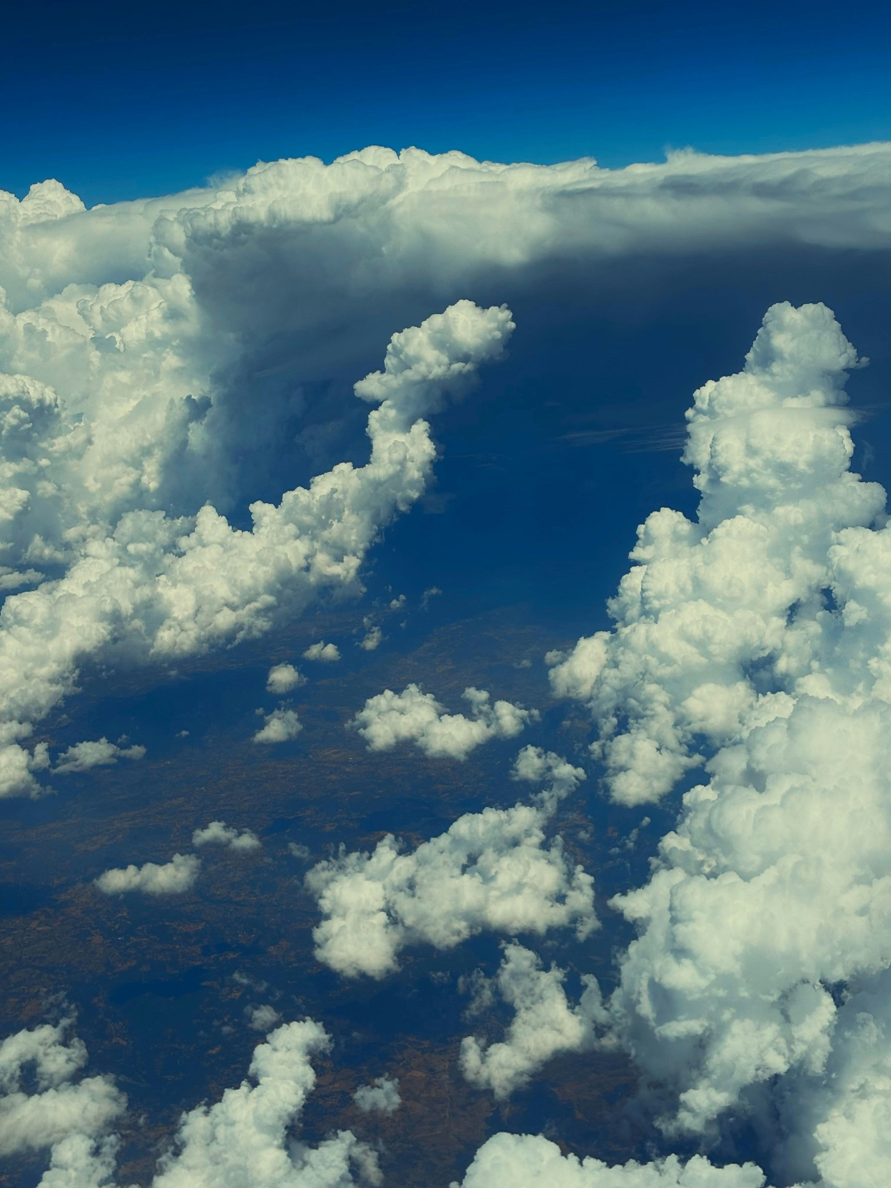 Expansive aerial view above a cloud deck with rugged terrain peeking through; high altitude atmosphere and bright cloud formations dominate the frame.