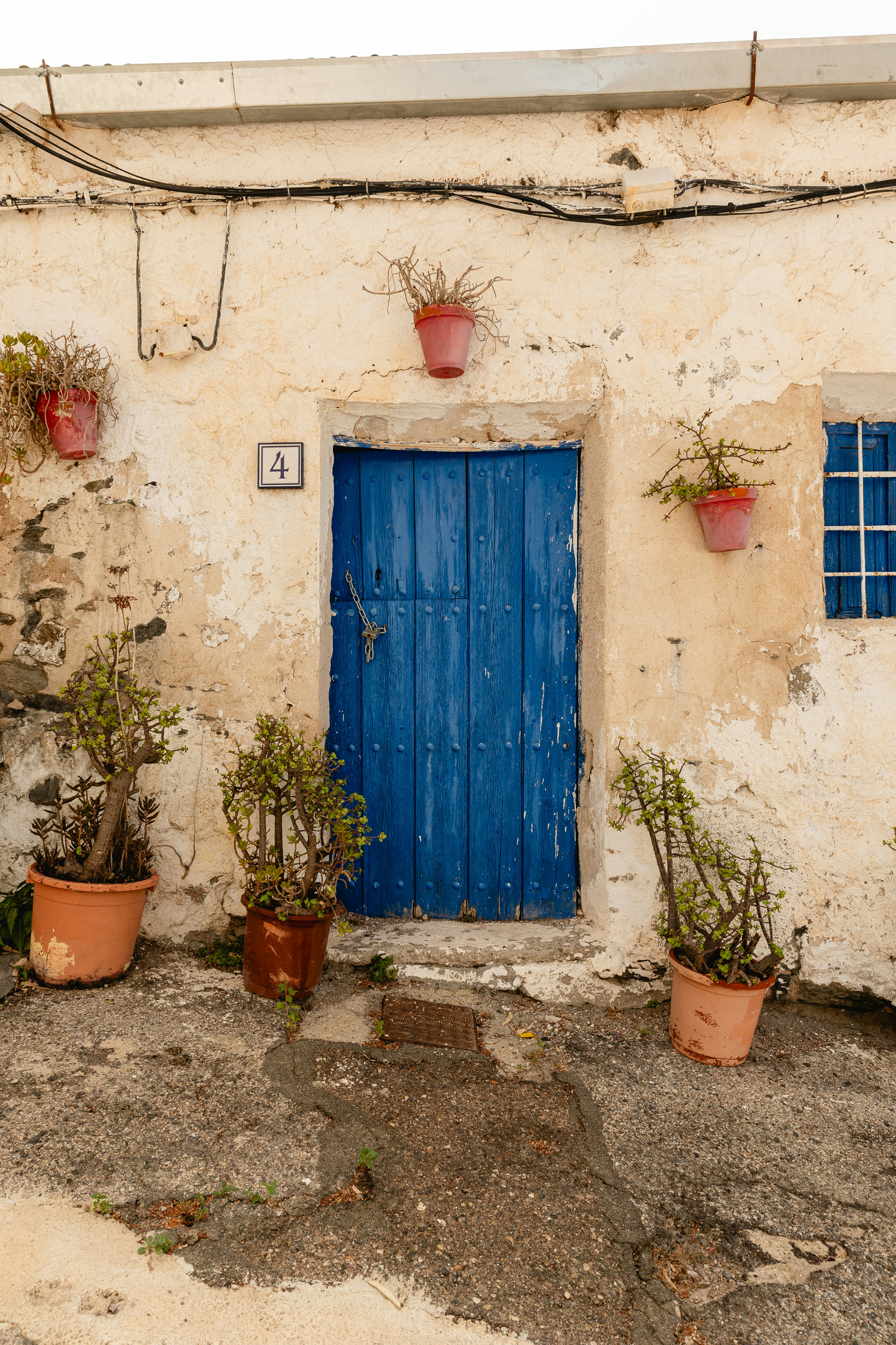 Blue Door Between Sunlit Pots on Aged Stucco
