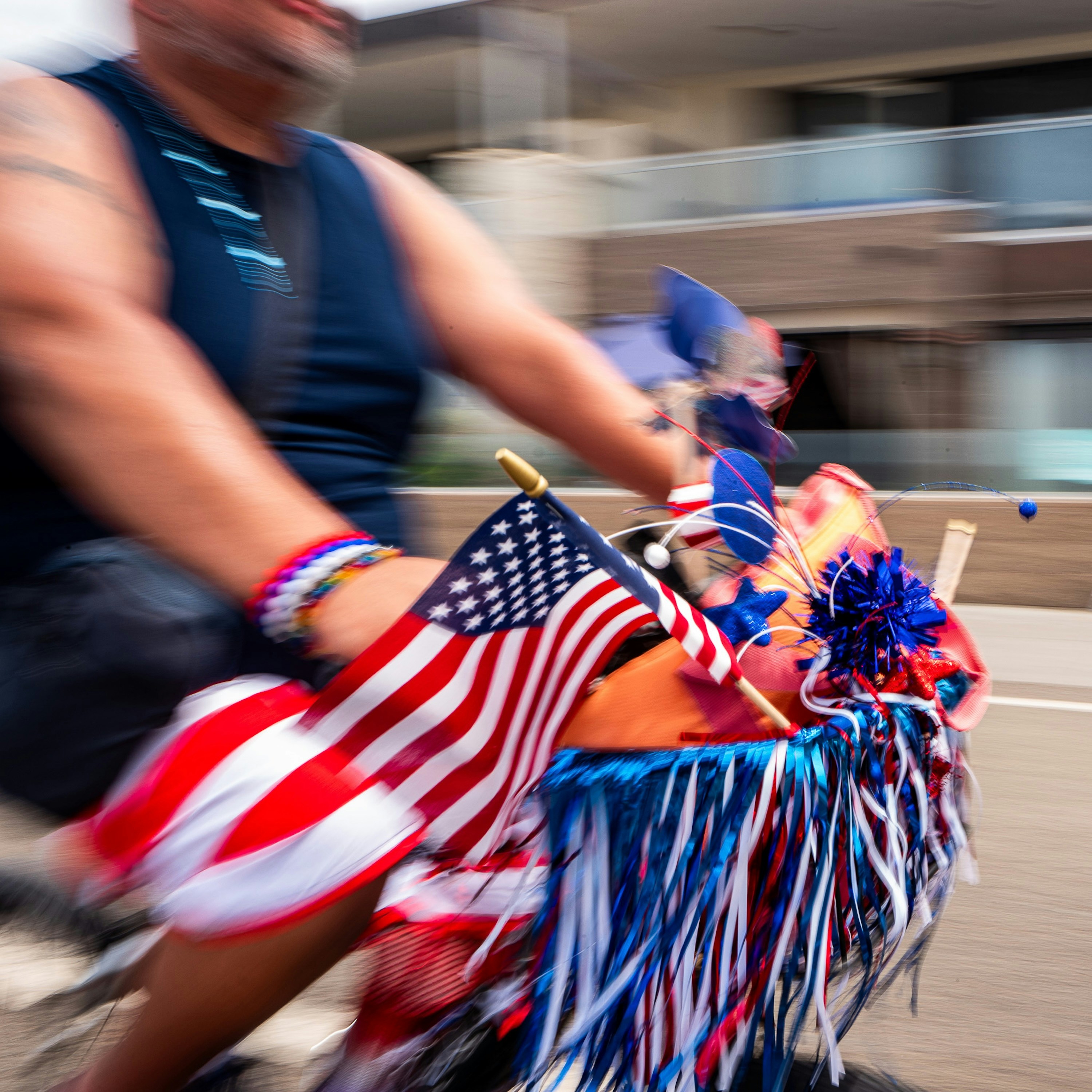 Motion-blurred rider with festive American flag decorations riding past a cityscape, capturing dynamic movement and patriotic colors.