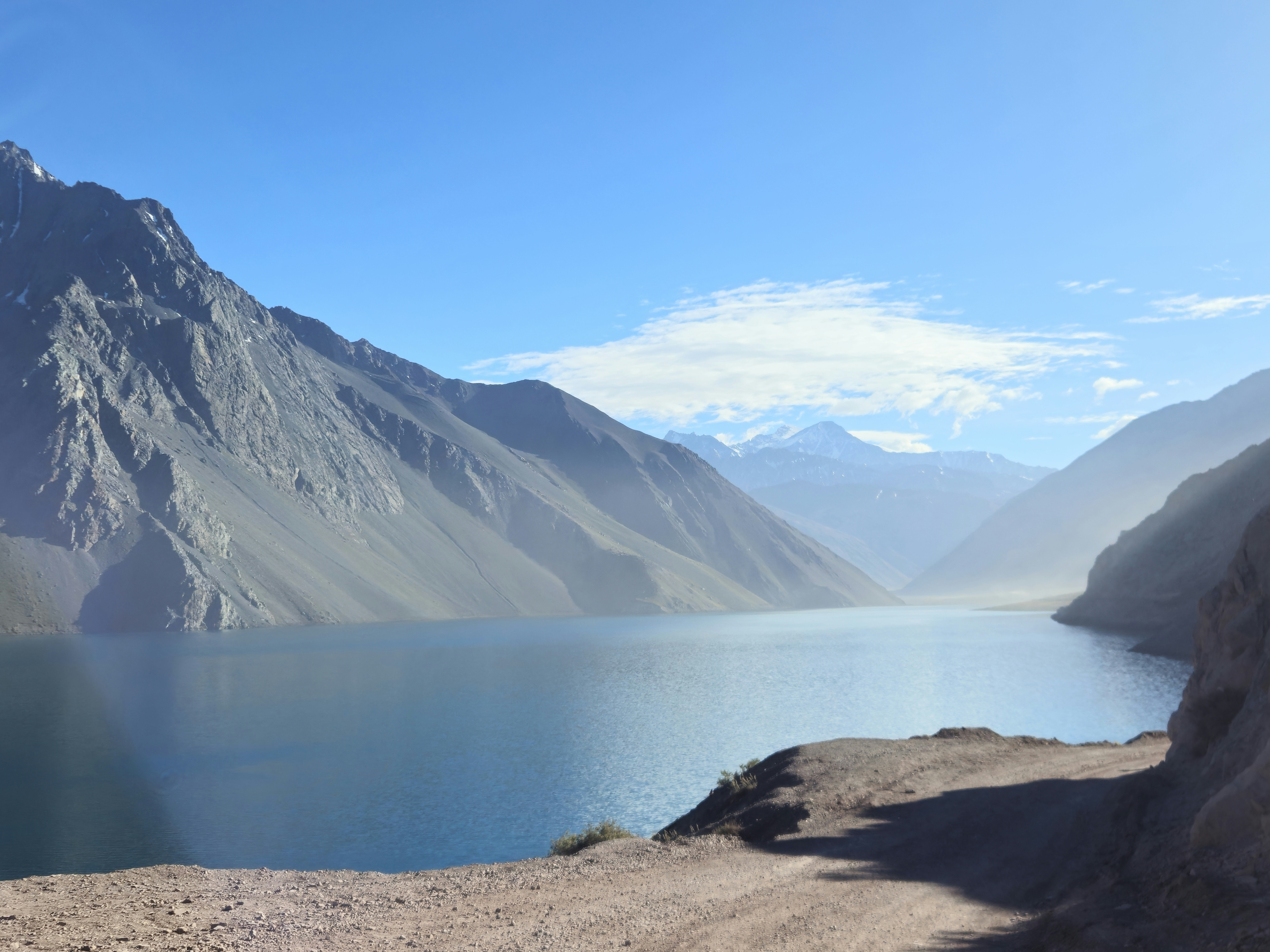 Still alpine lake mirrors towering valley walls under a clear blue sky in a remote mountain pass.