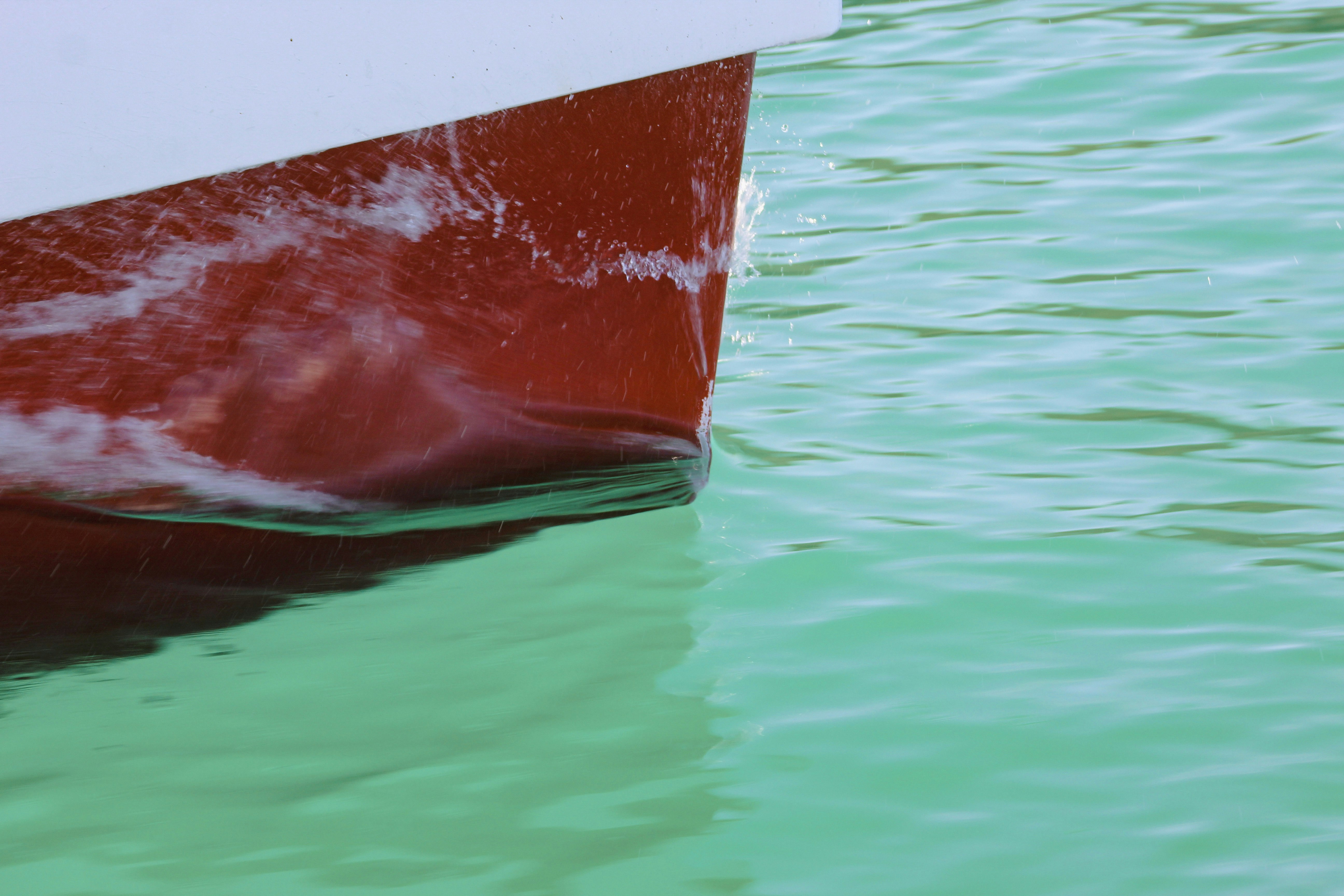 Red Hull at Turquoise Glimmer: A Close-Up of the Vessel’s Bow and Wake