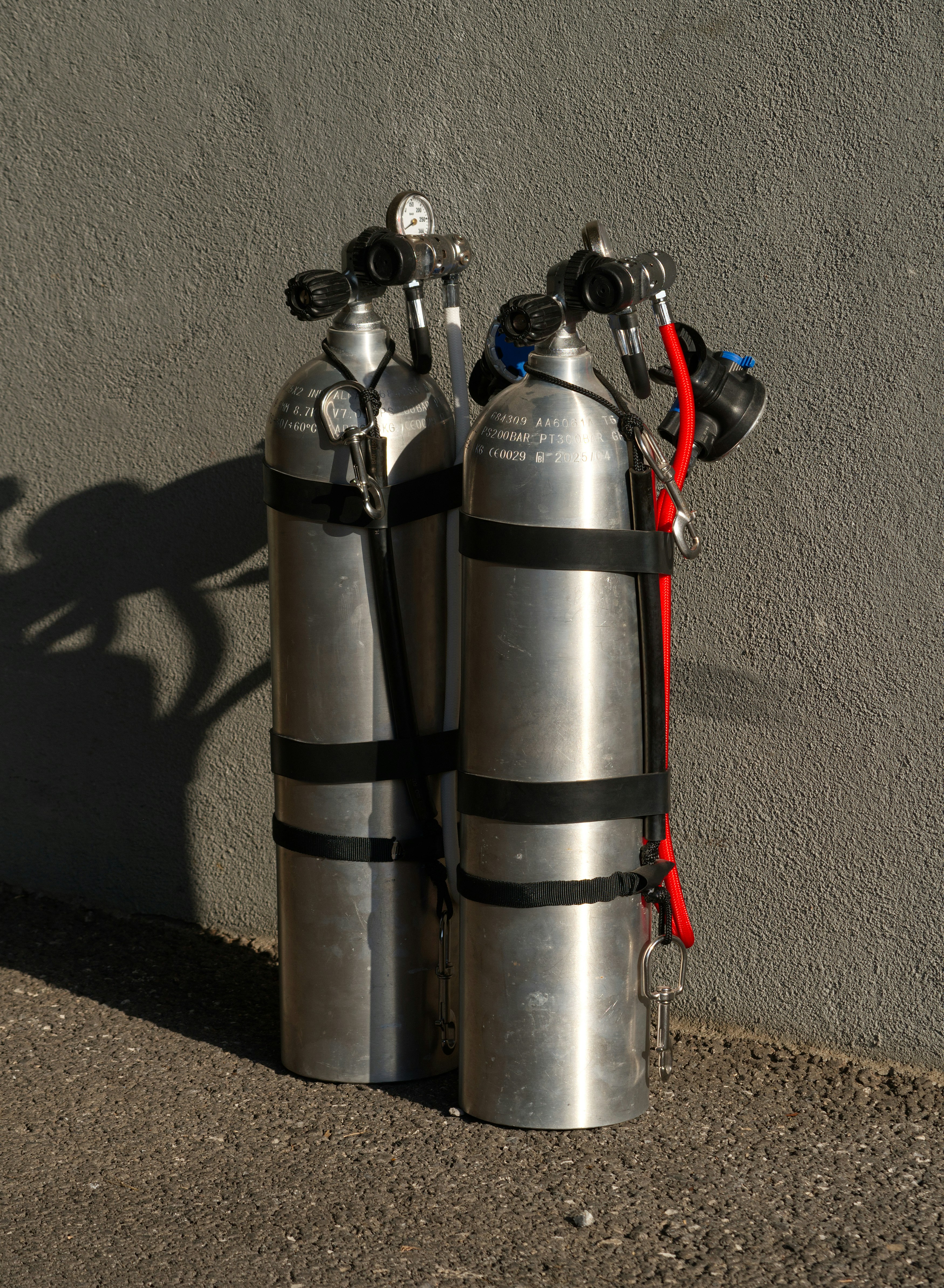 Twin Aluminum Cylinders Standby: A Sunlit Dive Pair Against a Rough Wall