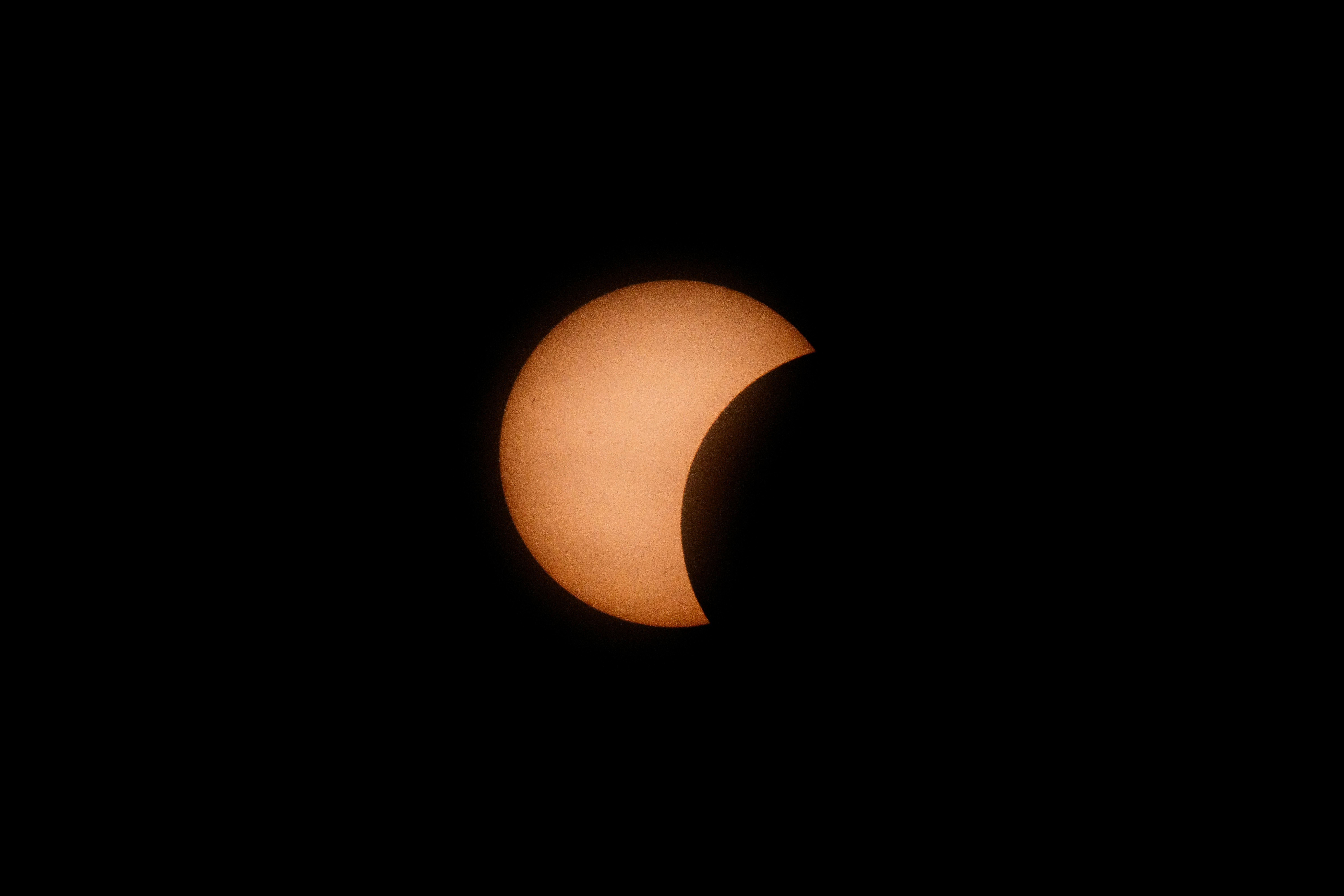 A partial solar eclipse showing a glowing orange crescent against a black sky.