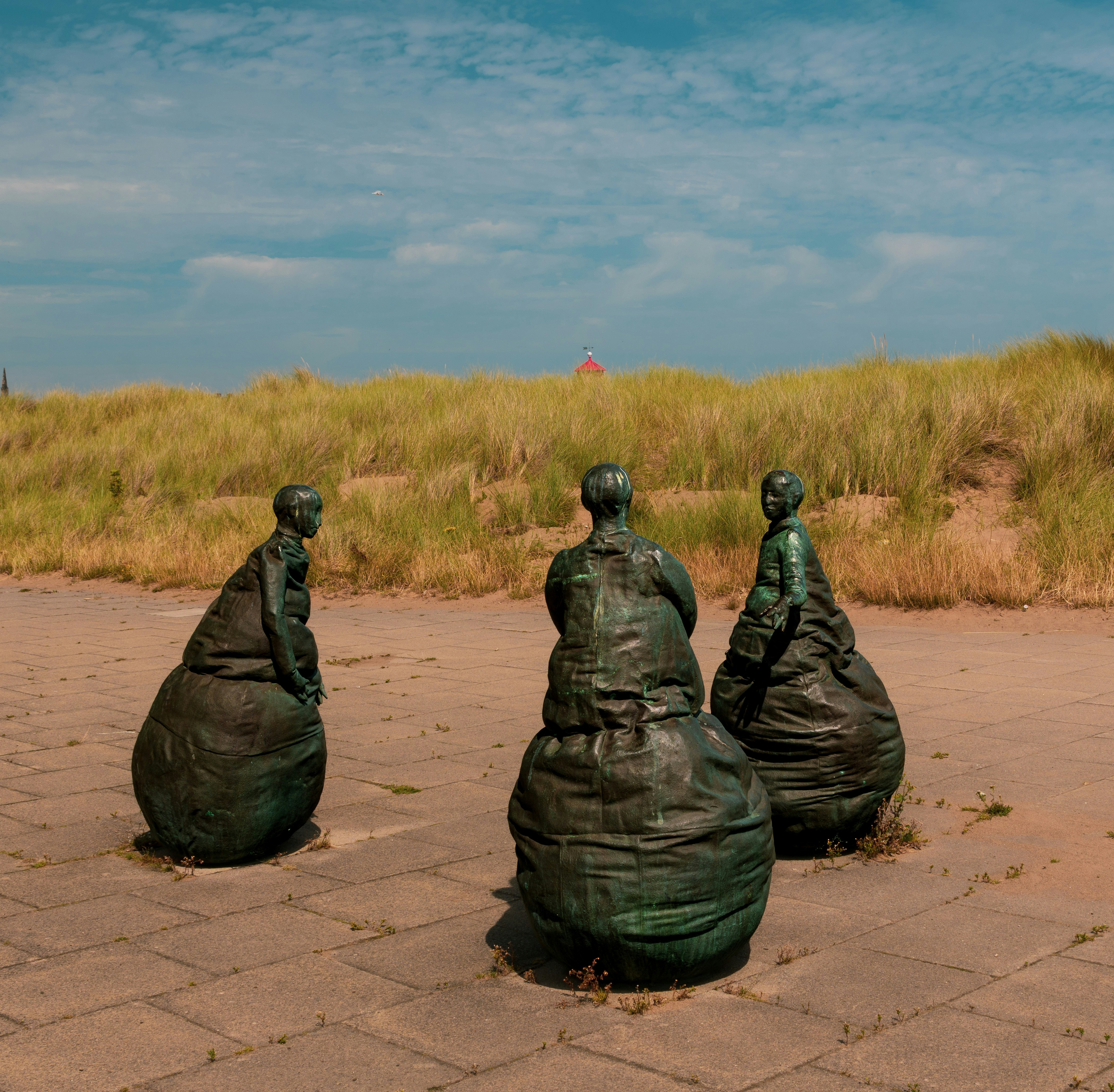 Three sculpted figures on a sunlit dune plaza