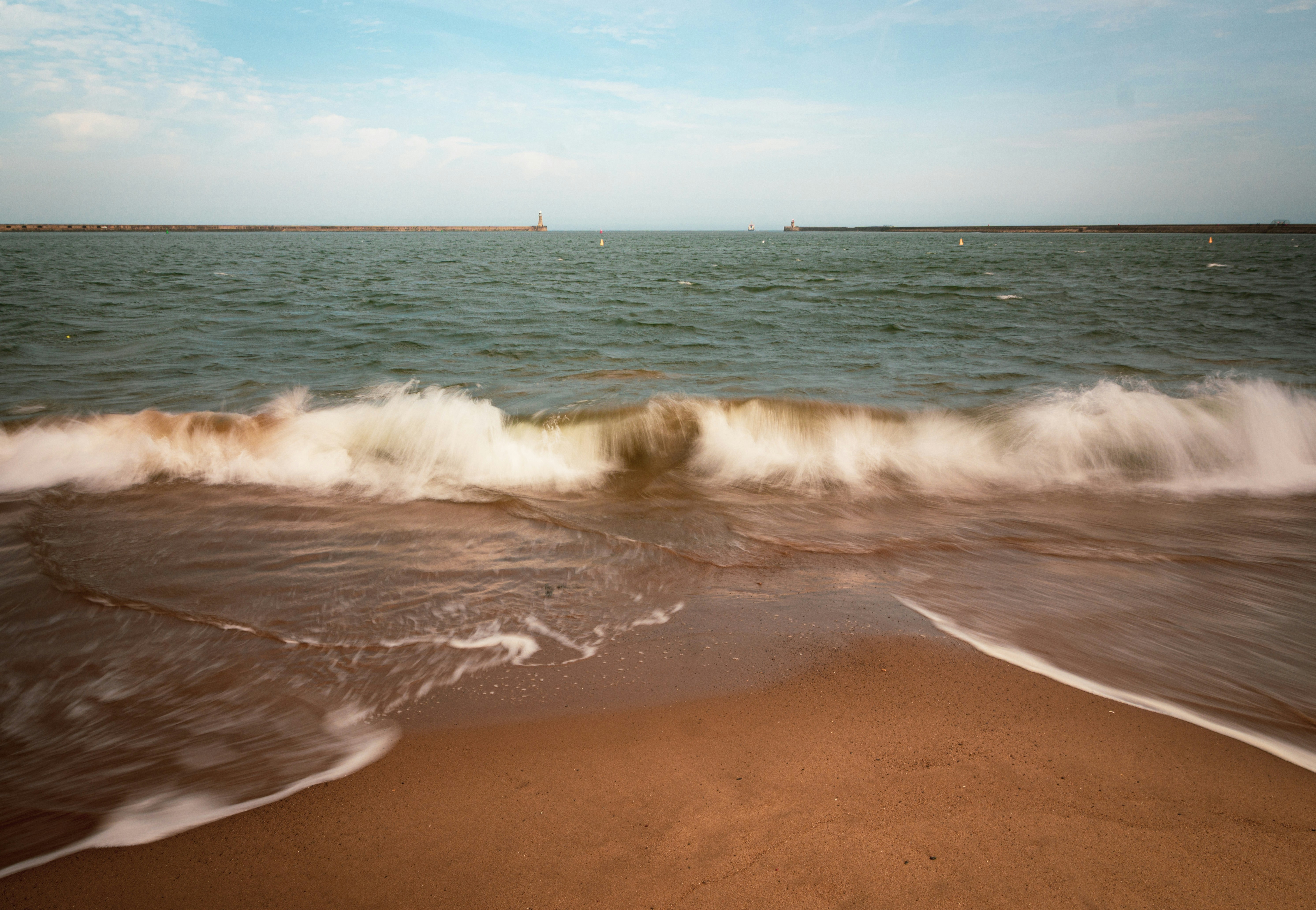 Foamy shoreline over a quiet sea under a soft-blue sky