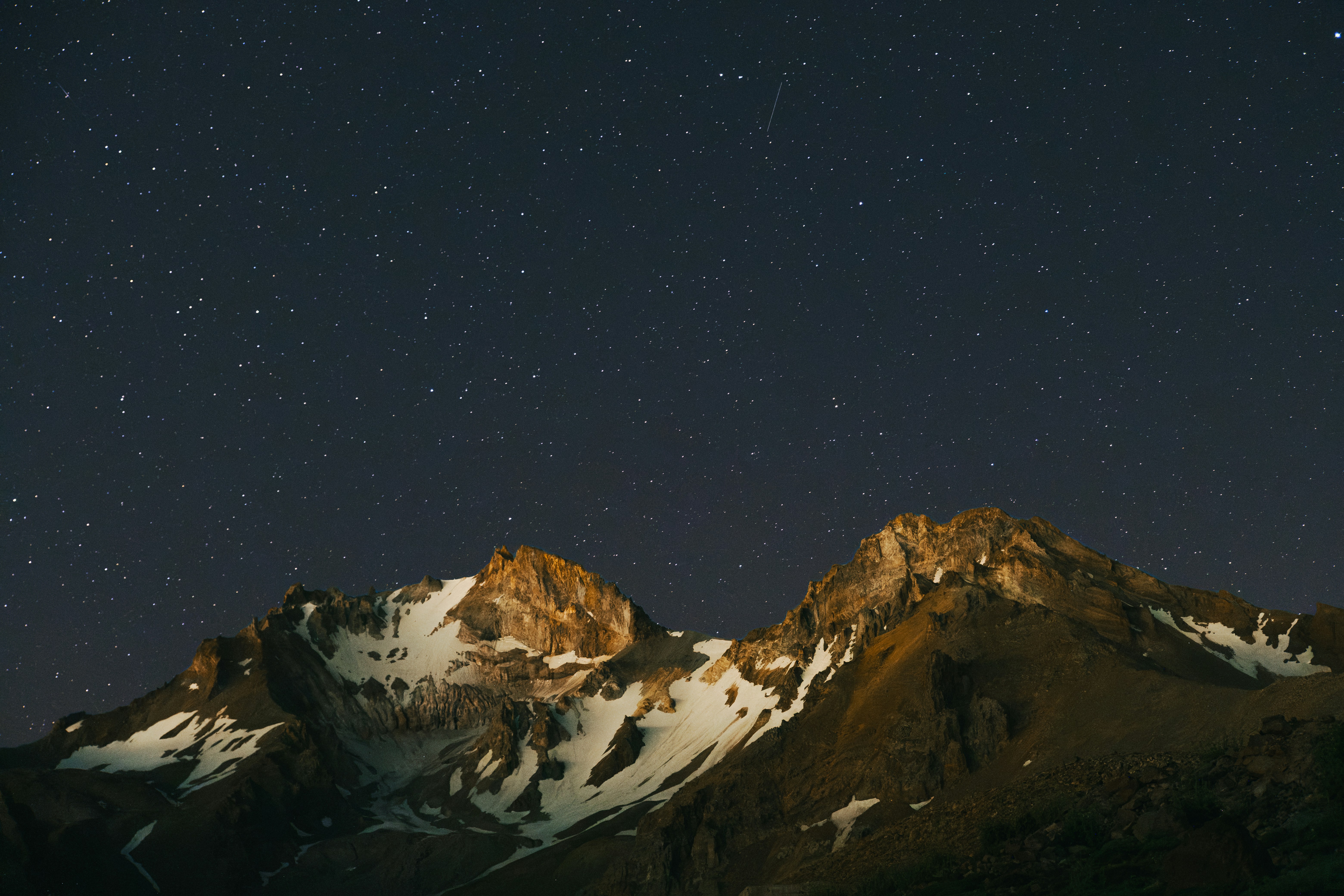 Snow-capped mountains beneath a clear star-filled night sky, capturing the quiet alpine majesty.