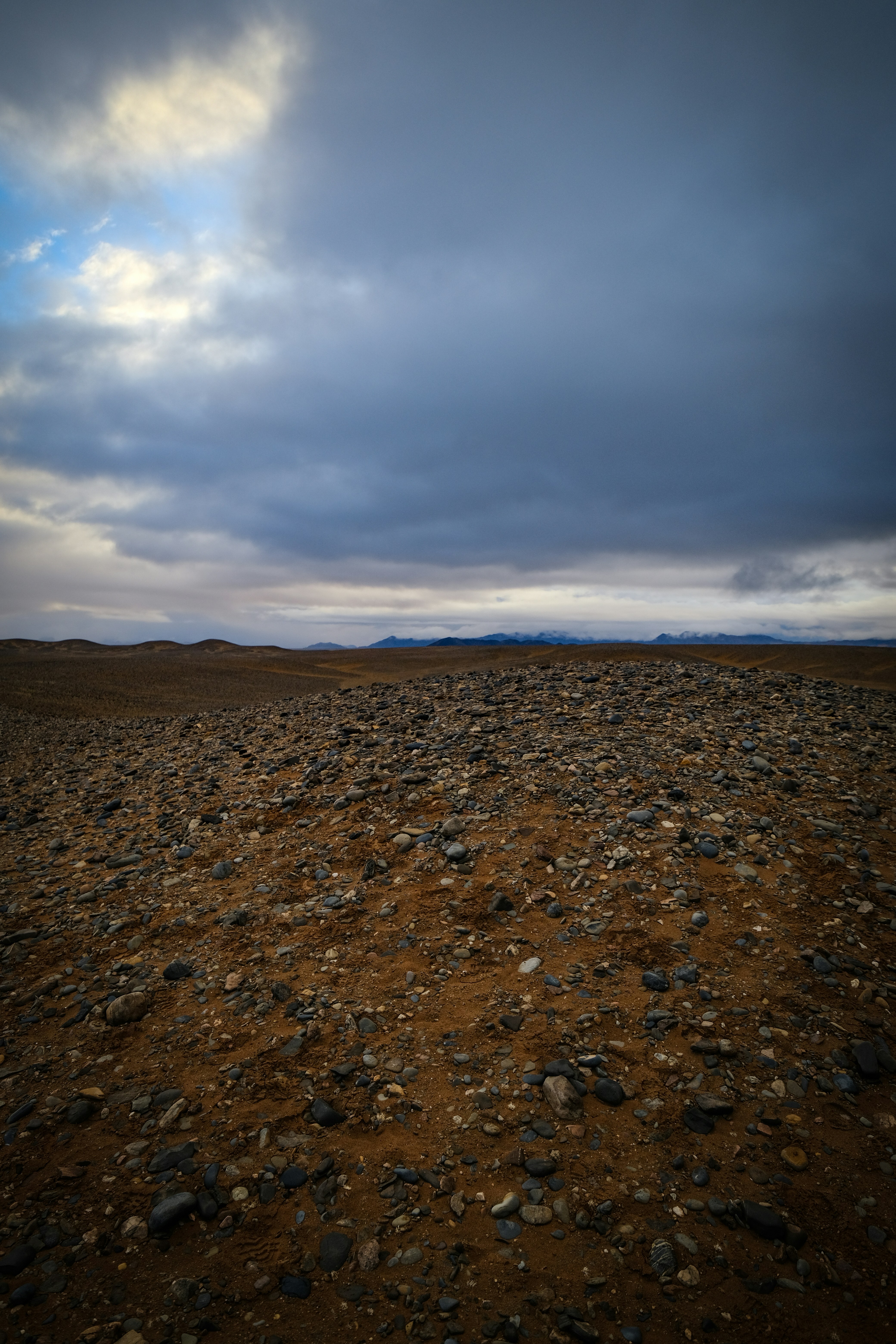 Rock-strewn dirt road to distant blue horizon under brooding clouds