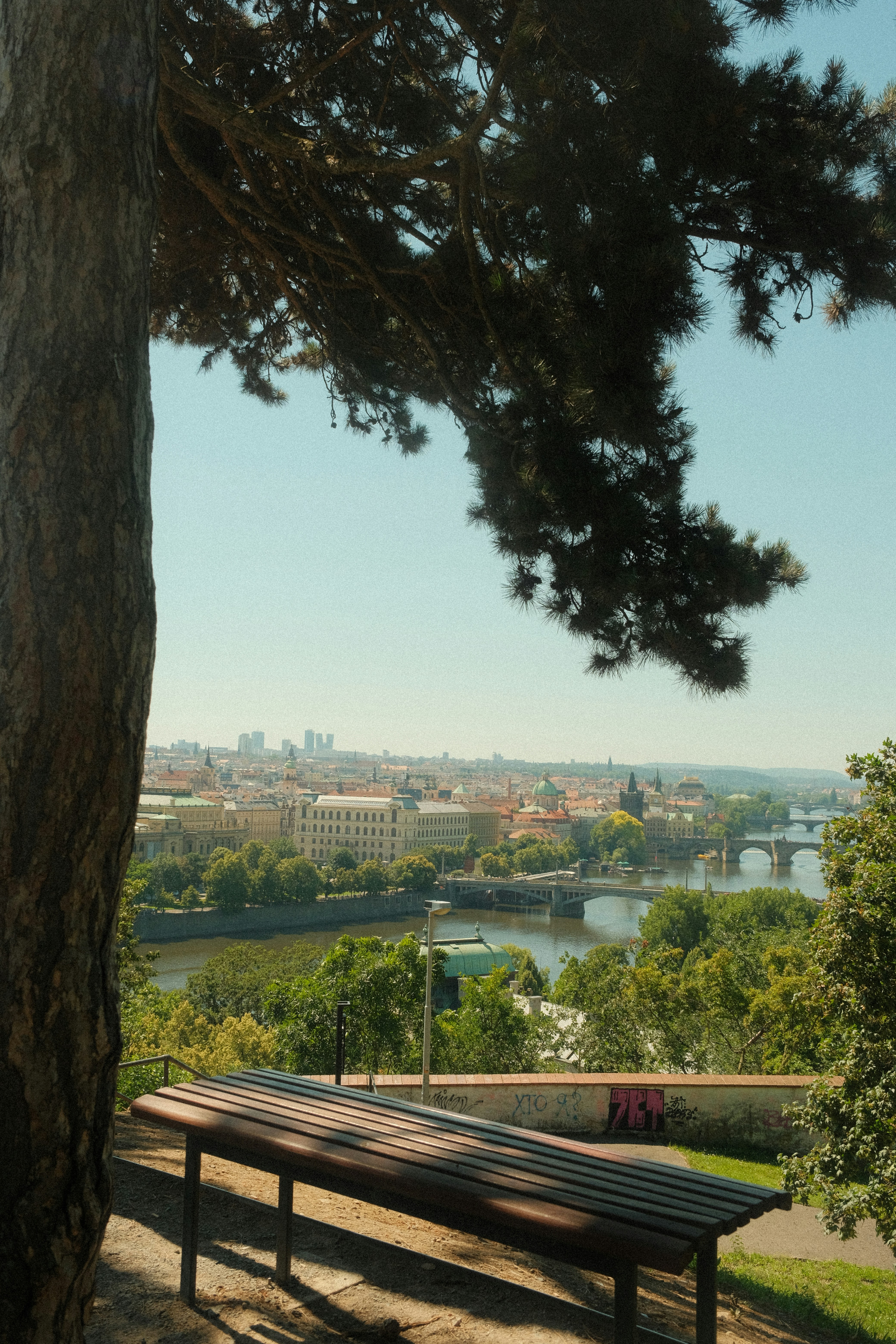 An empty park bench offering a scenic vantage point over the Vltava River and the historic cityscape of Prague.