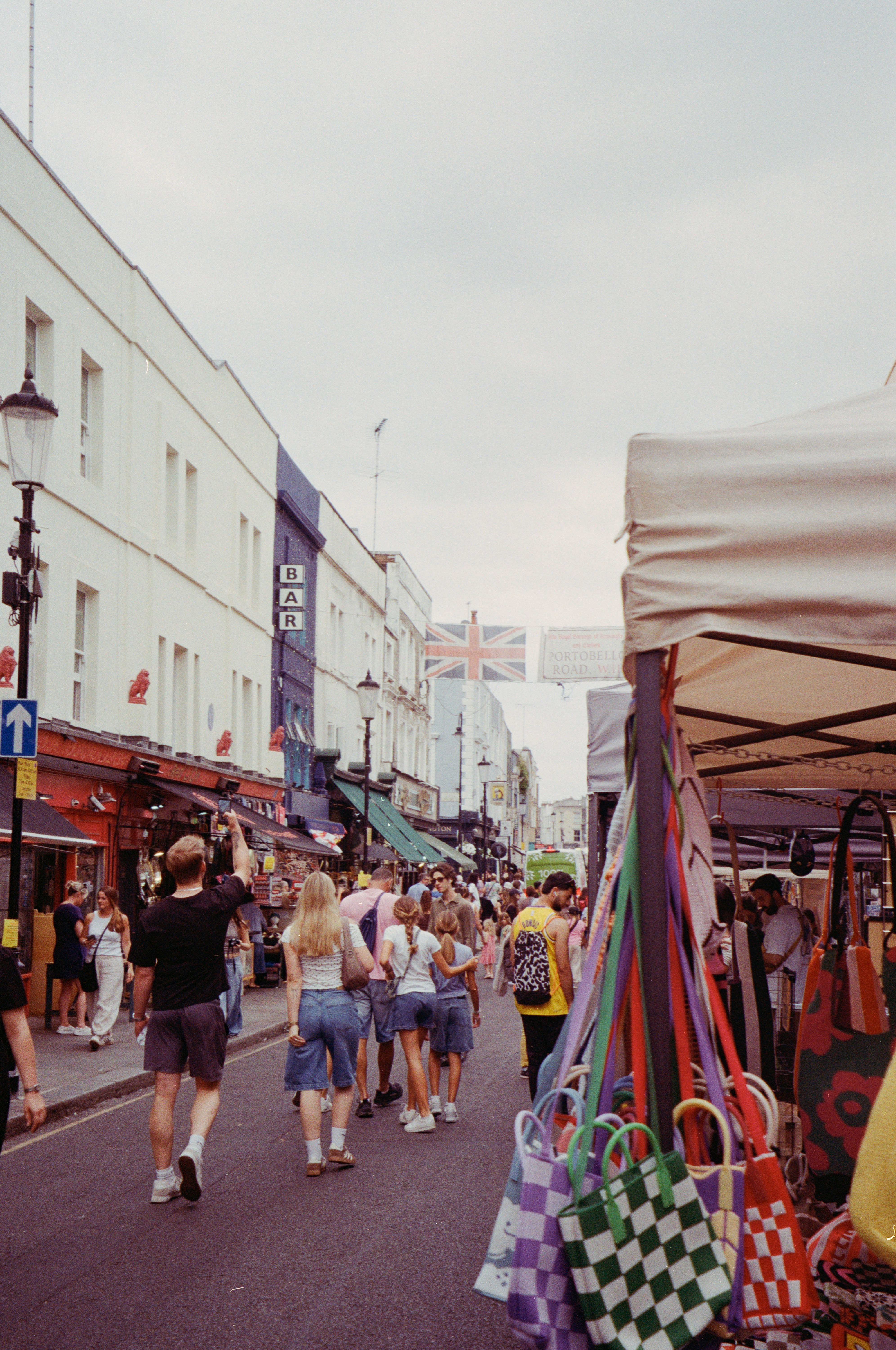 Crowded High Street in Summer Market with Colorful Tote Stall