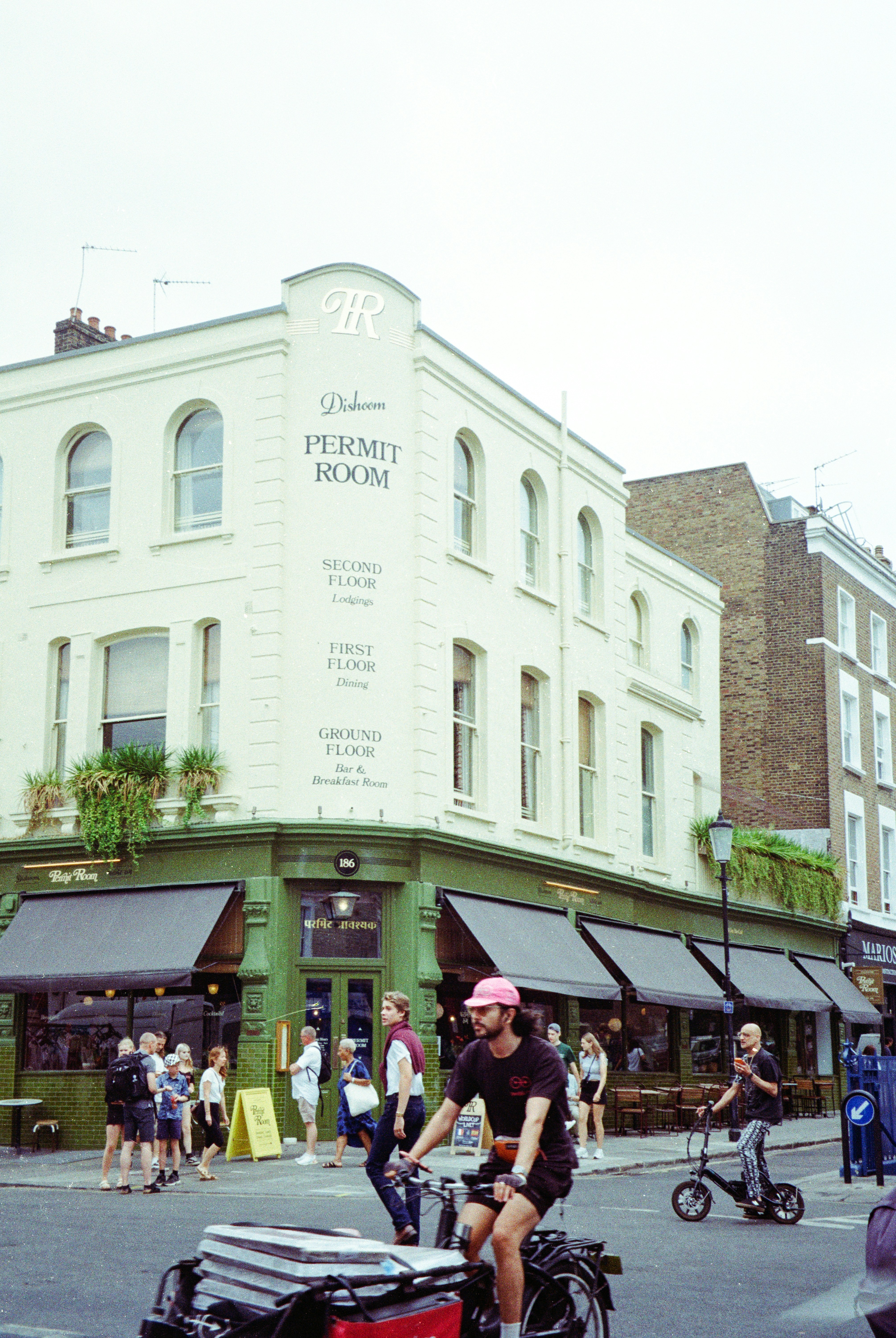 Urban Pedal and Pastry: Pedestrians and cyclists in front of a pastel corner pub