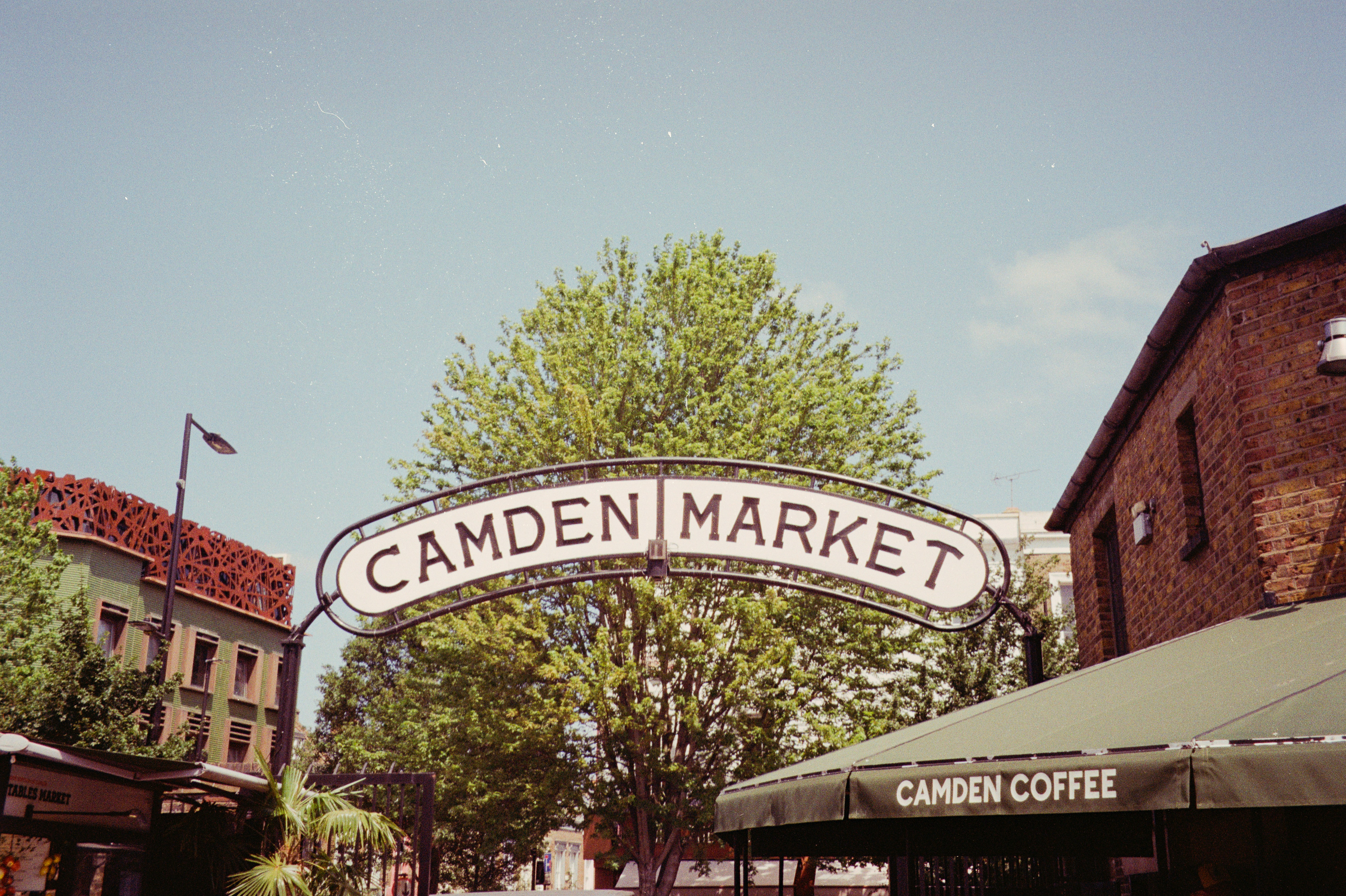 Archway to Camden: Market Sign Framed by Trees and Café Canopy