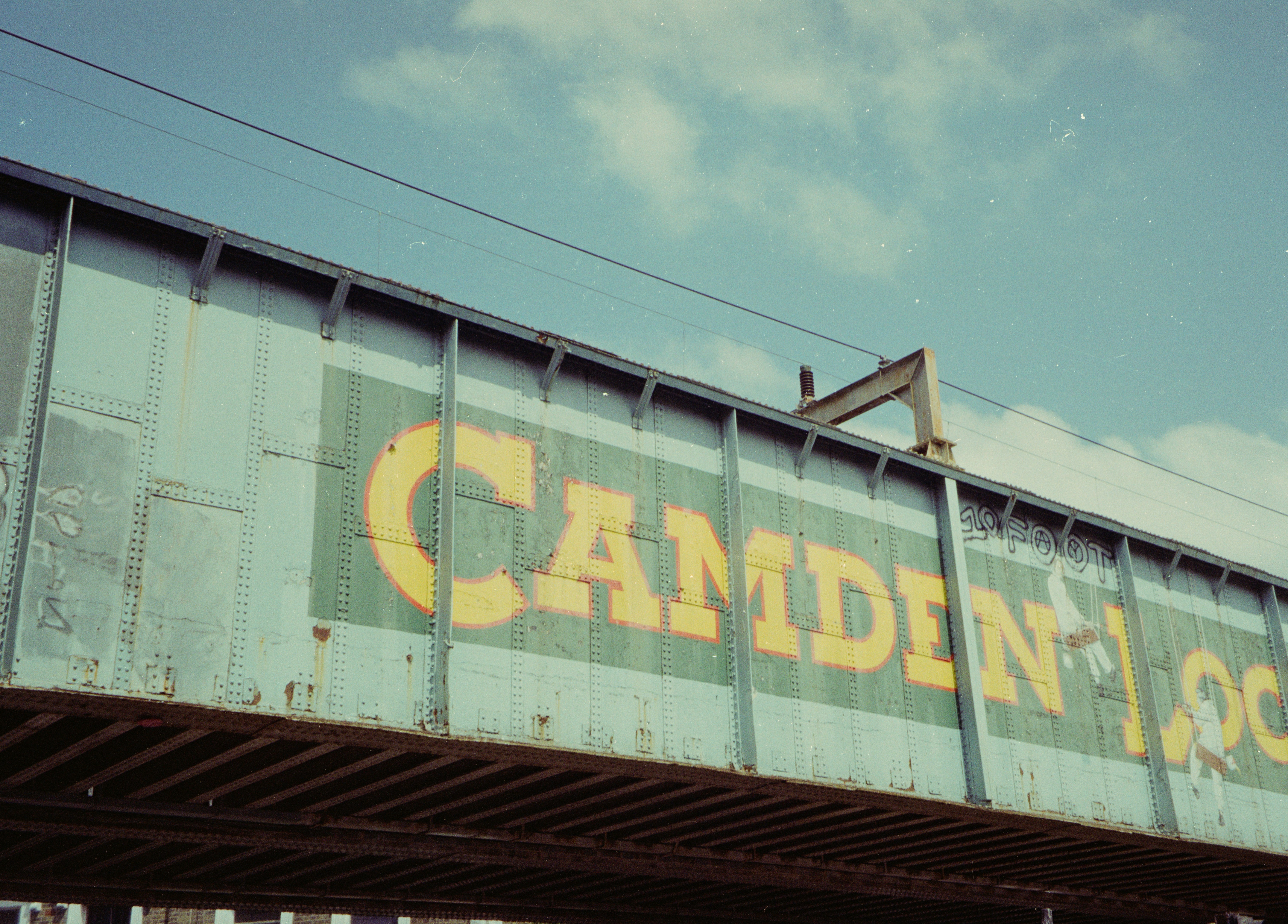 A metal railway bridge with the words Camden Lock painted in yellow letters