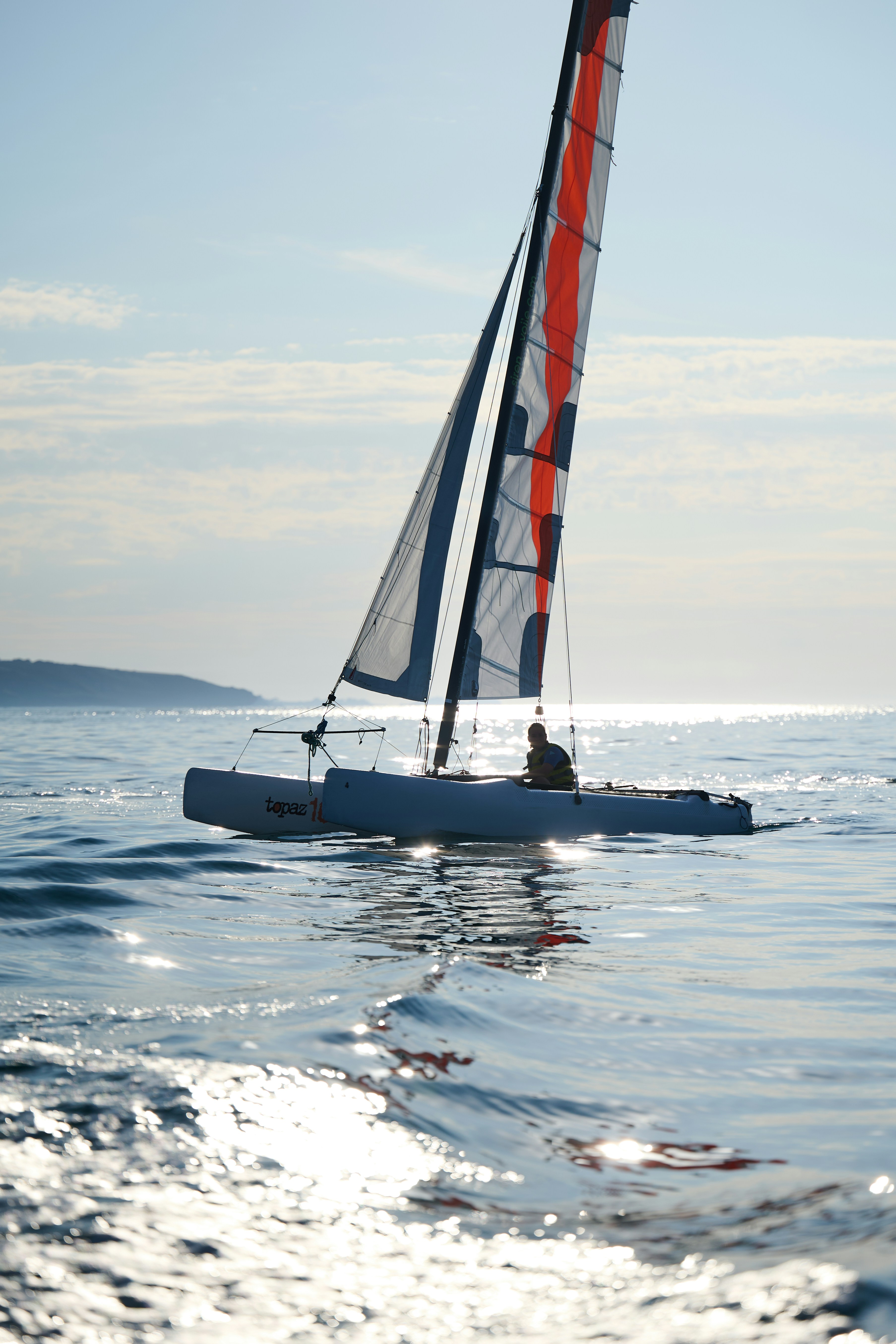 Sailing Silhouette: A Solo Sailboat Glides Across Sunlit Seas