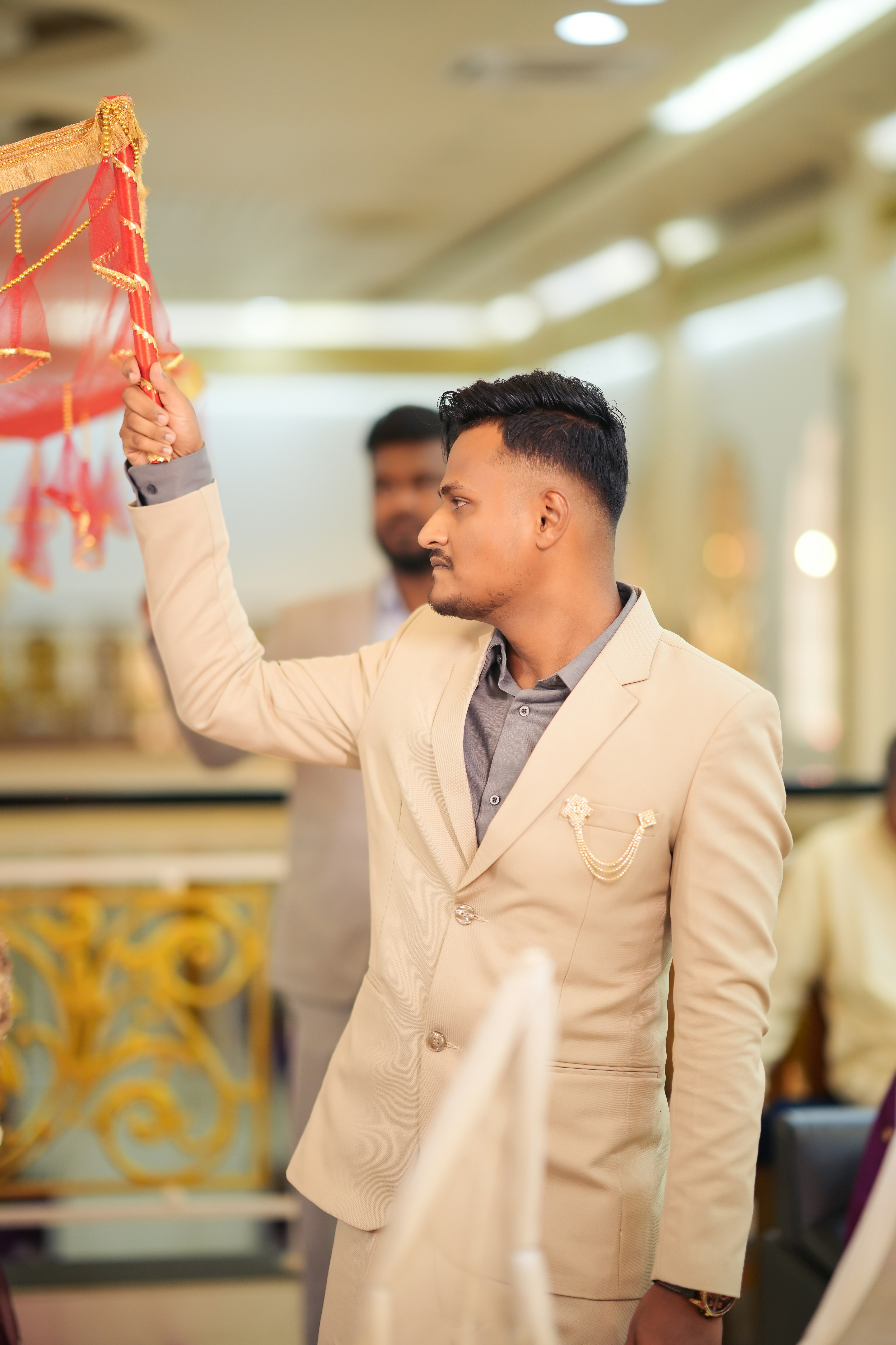 Groomed Groom in a Cream Suit Lifts a decorative Flag in a Bright Indoor Ceremony