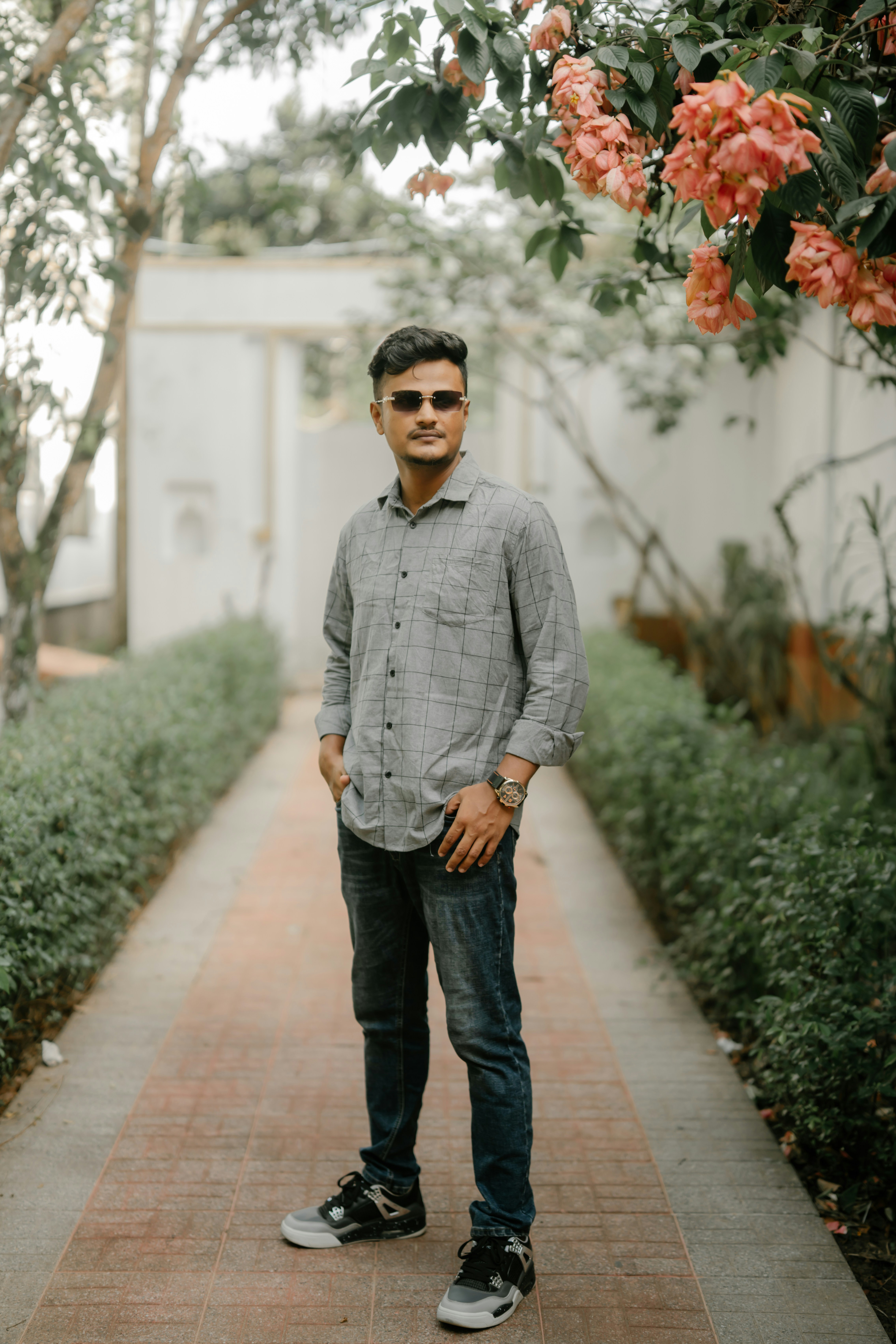 Urban portrait under bloom: a man in a checked shirt standing along a garden path