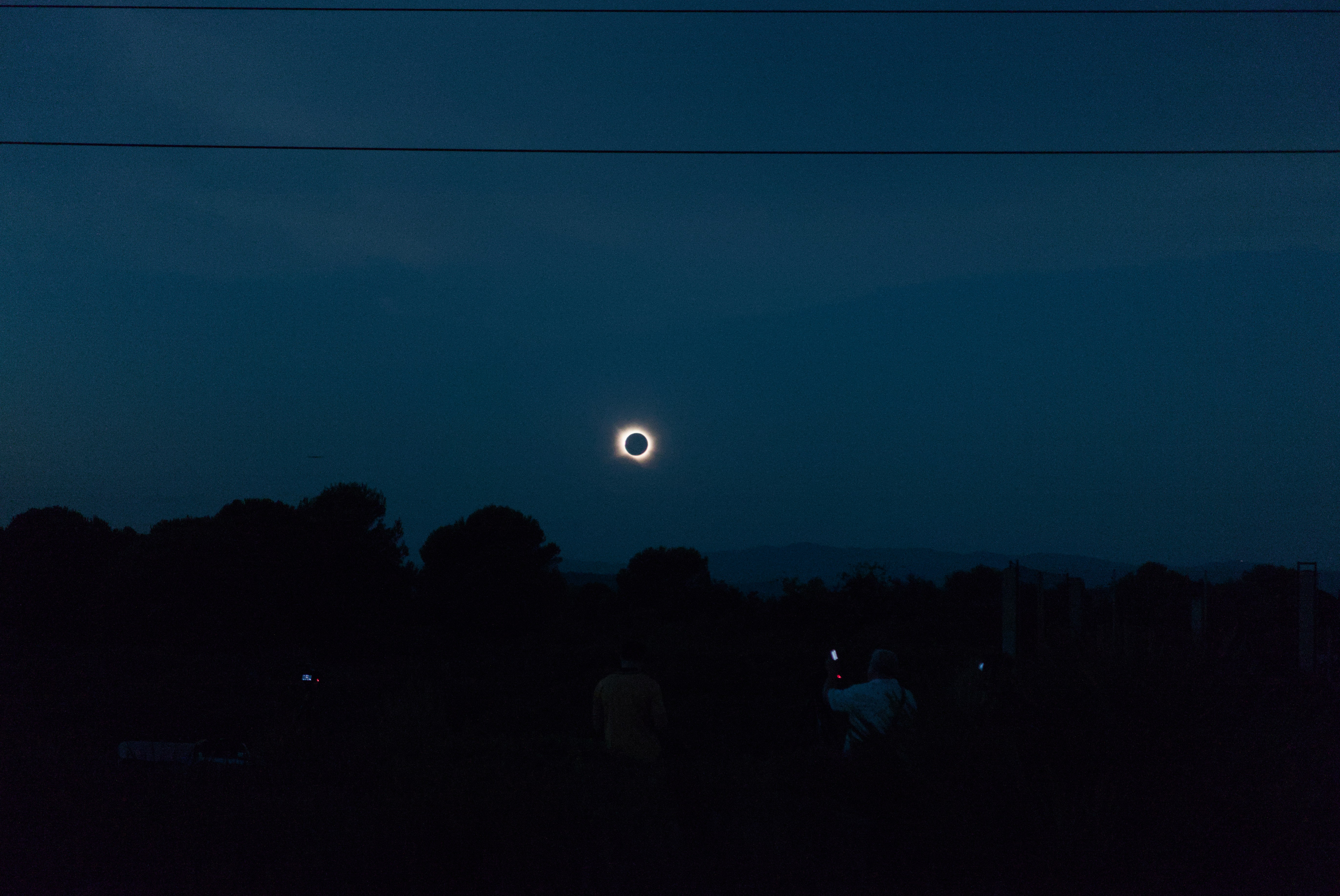 A dark landscape under a night sky with a solar eclipse halo centered above distant silhouettes.