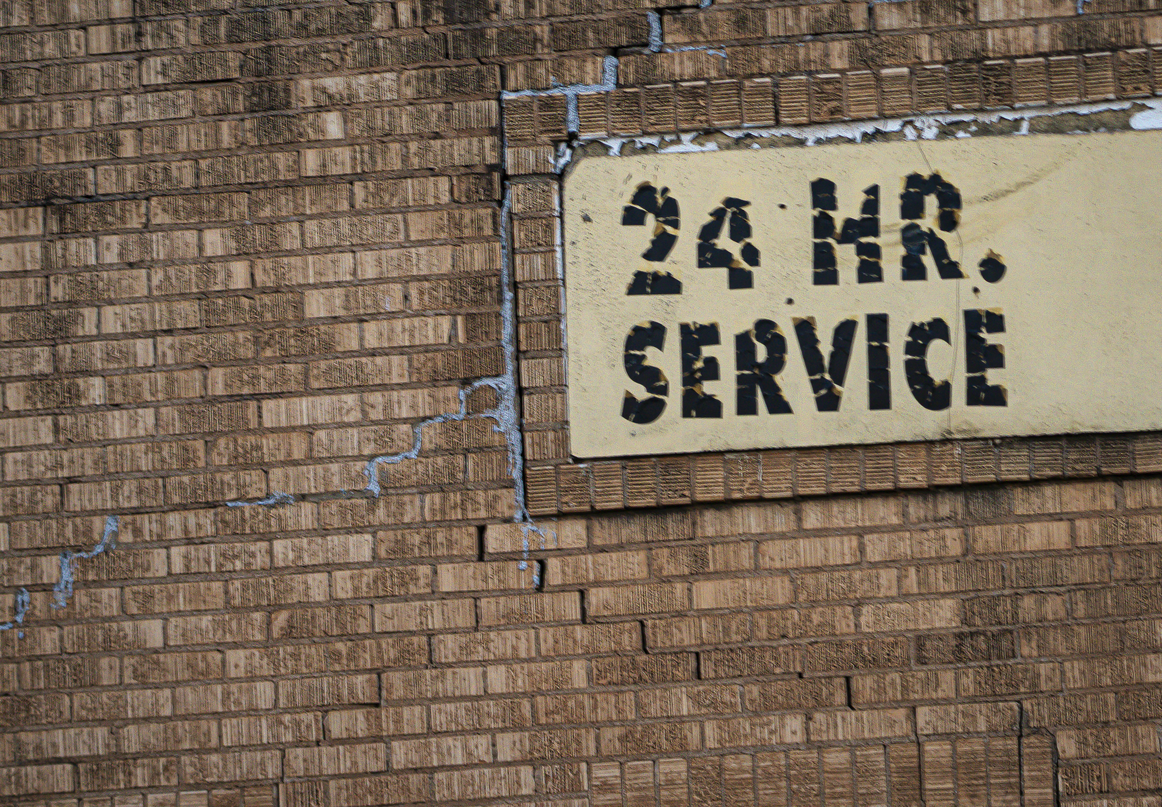 Weathered brick wall with a faded rectangular sign reading '28 MR. SERVICE' mounted on the surface.