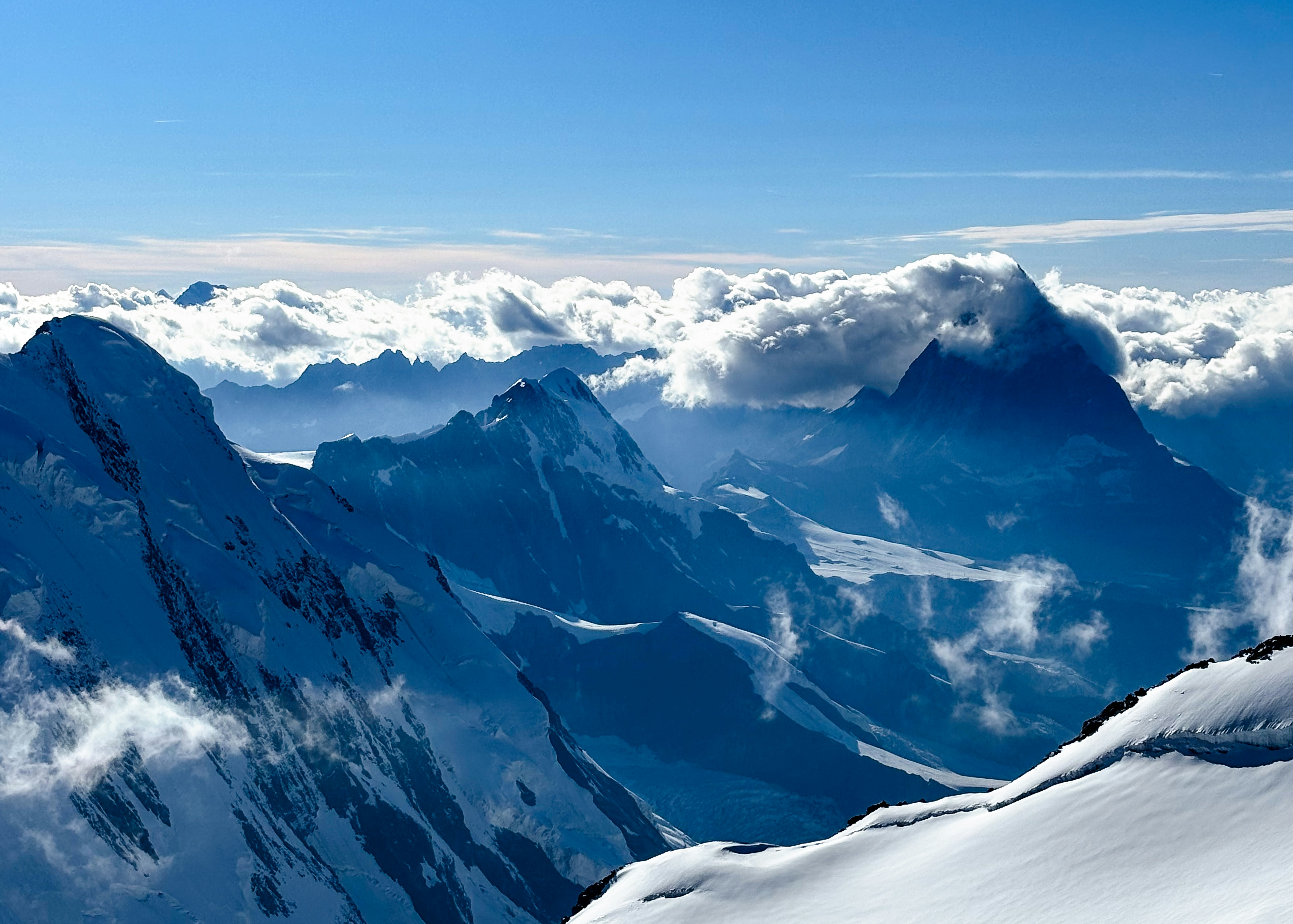 Snowy alpine crests rise under a blue sky with dramatic clouds, conveying the vast, crisp beauty of high-altitude terrain.