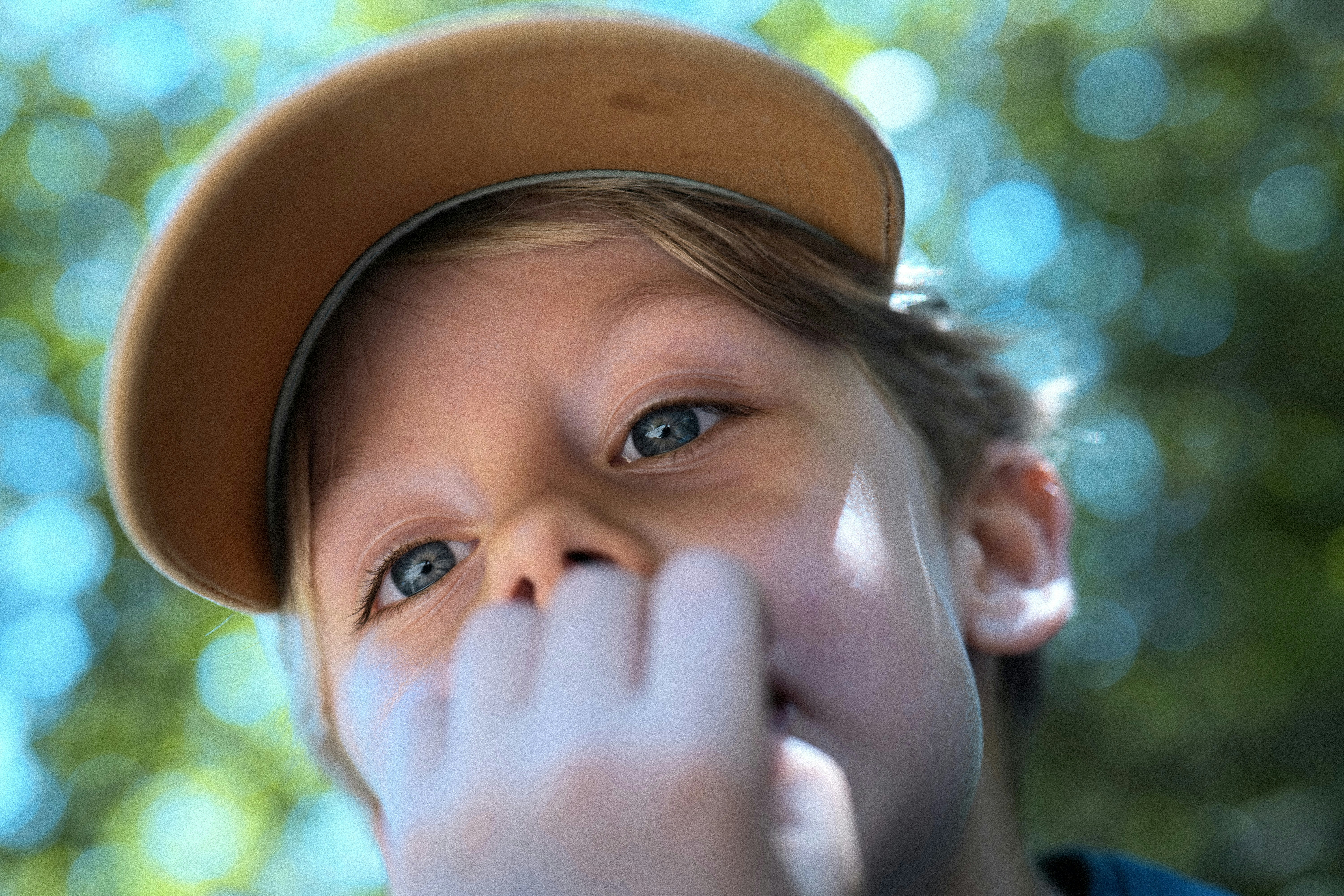 Close-up of a child wearing a cap, looking toward the camera with a vivid blue sky bokeh behind; a candid portrait emphasizing facial expression and depth of field.