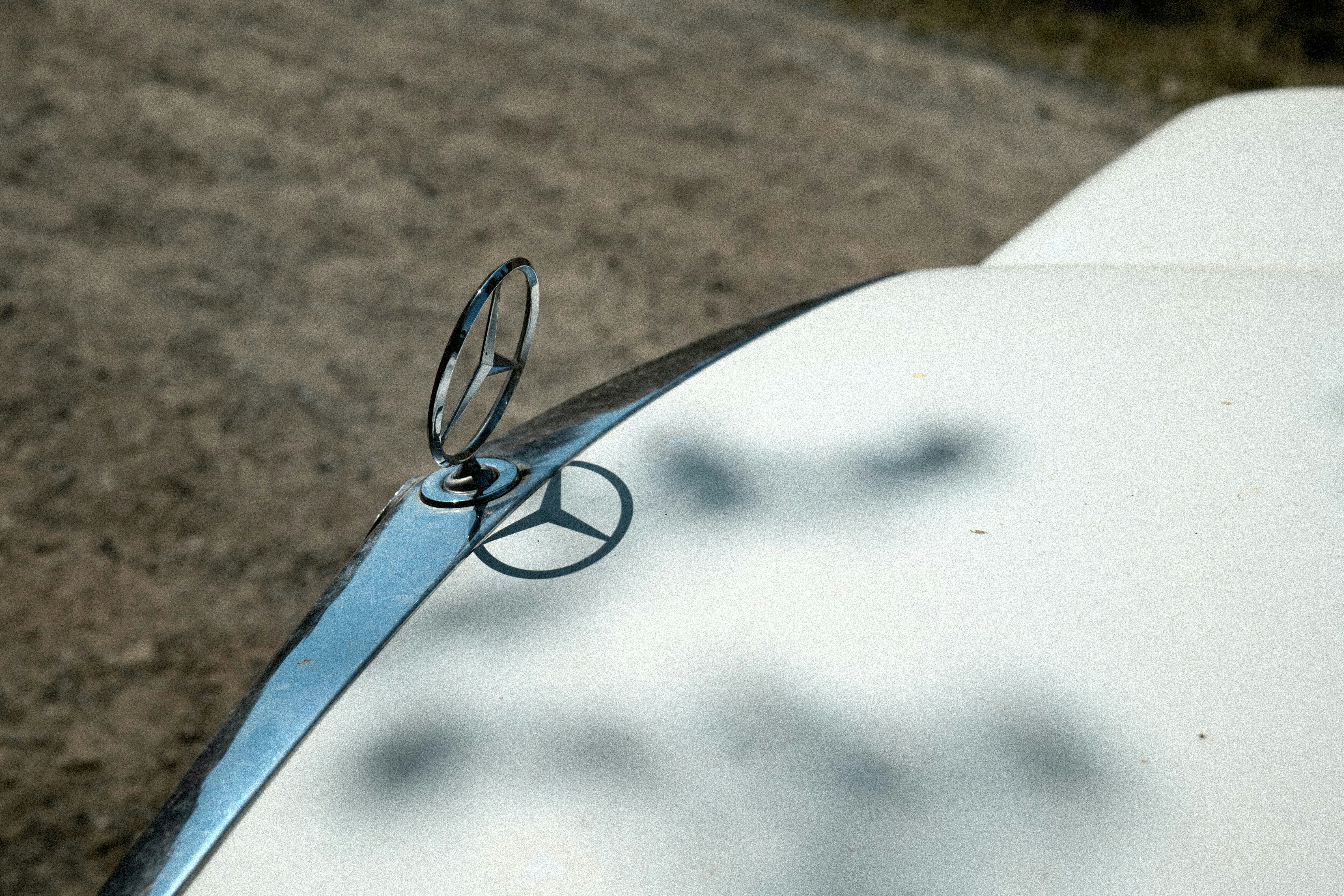 Mercedes hood ornament catching sunlight on weathered surface
