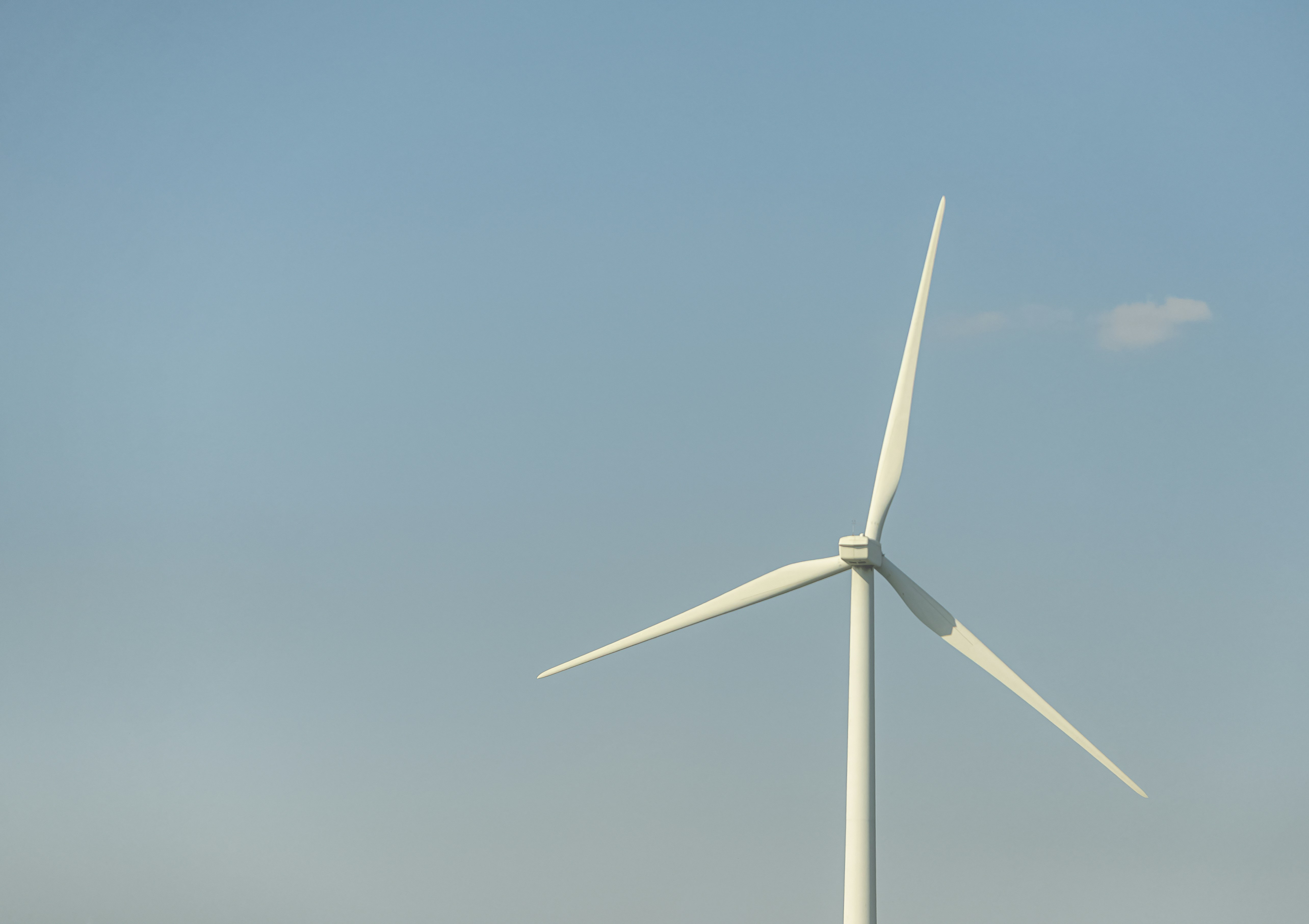 Tall wind turbine set against a pale blue sky, blades angled gracefully as the structure dominates the frame.