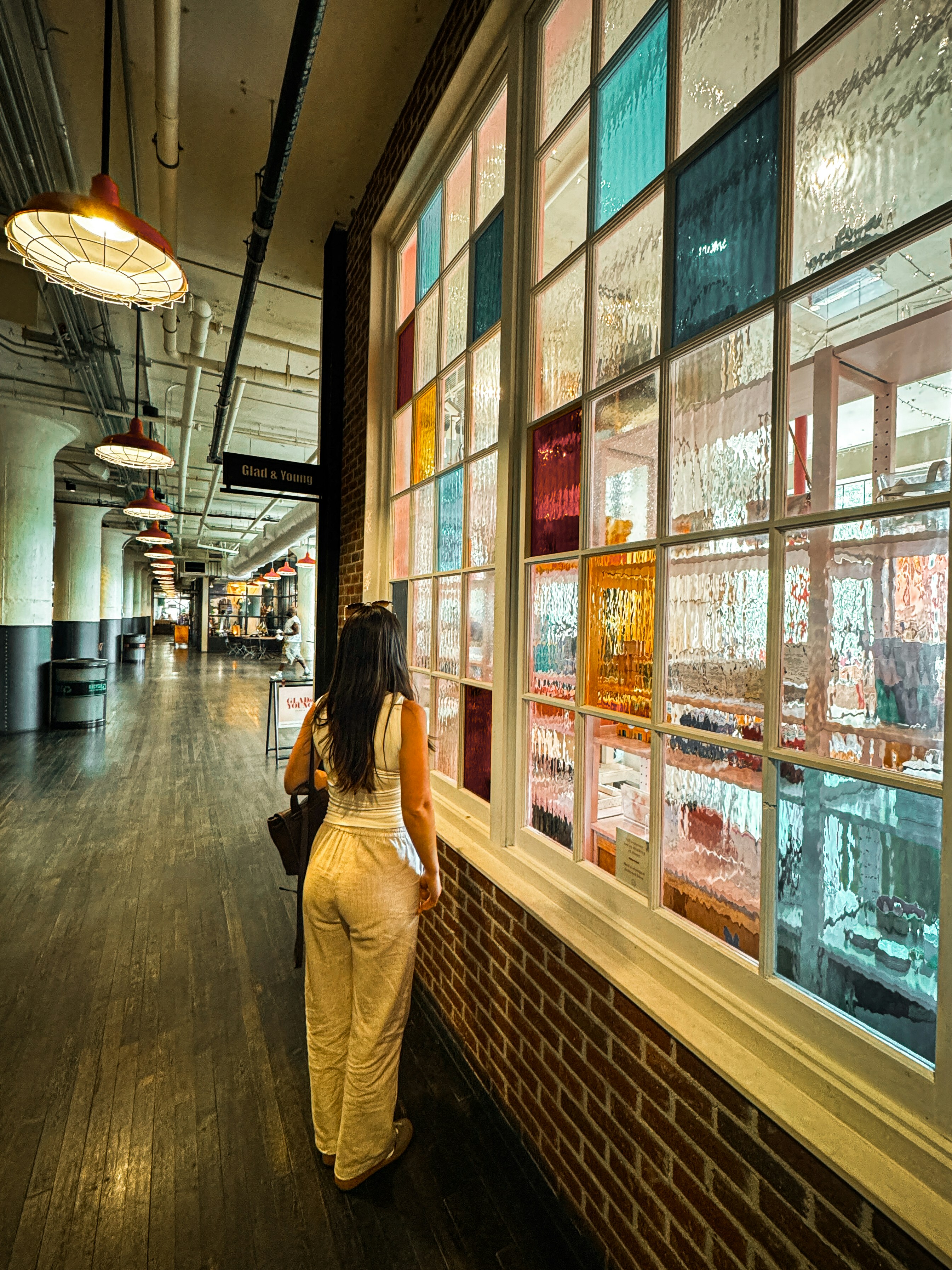 Colorful Corridor Muse: A Woman Walks Beside a Glass Wall Mosaic