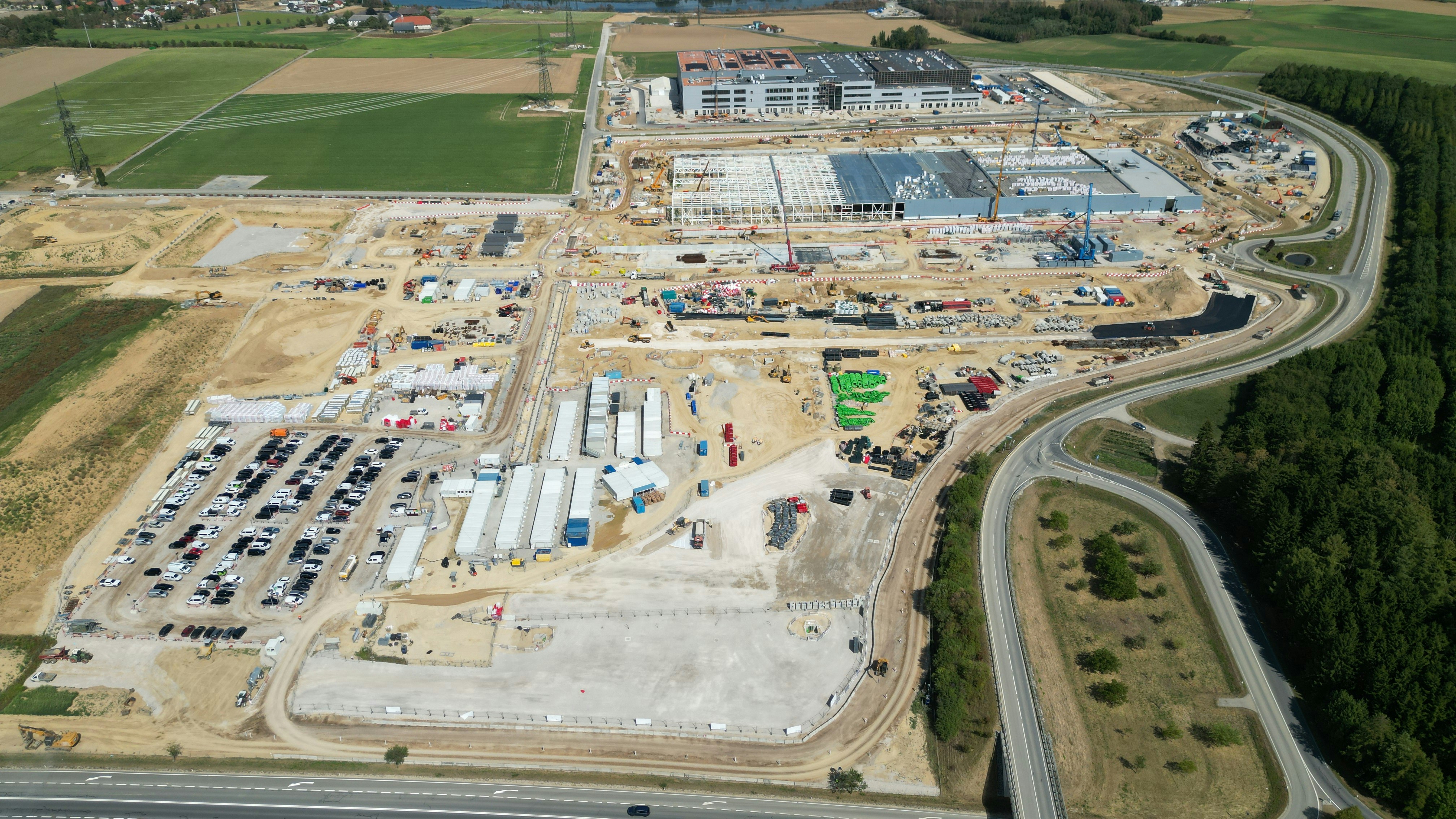 Active construction site with multiple buildings under progress and surrounding roads visible from above. Aerial view highlights ongoing development and layout of facilities.