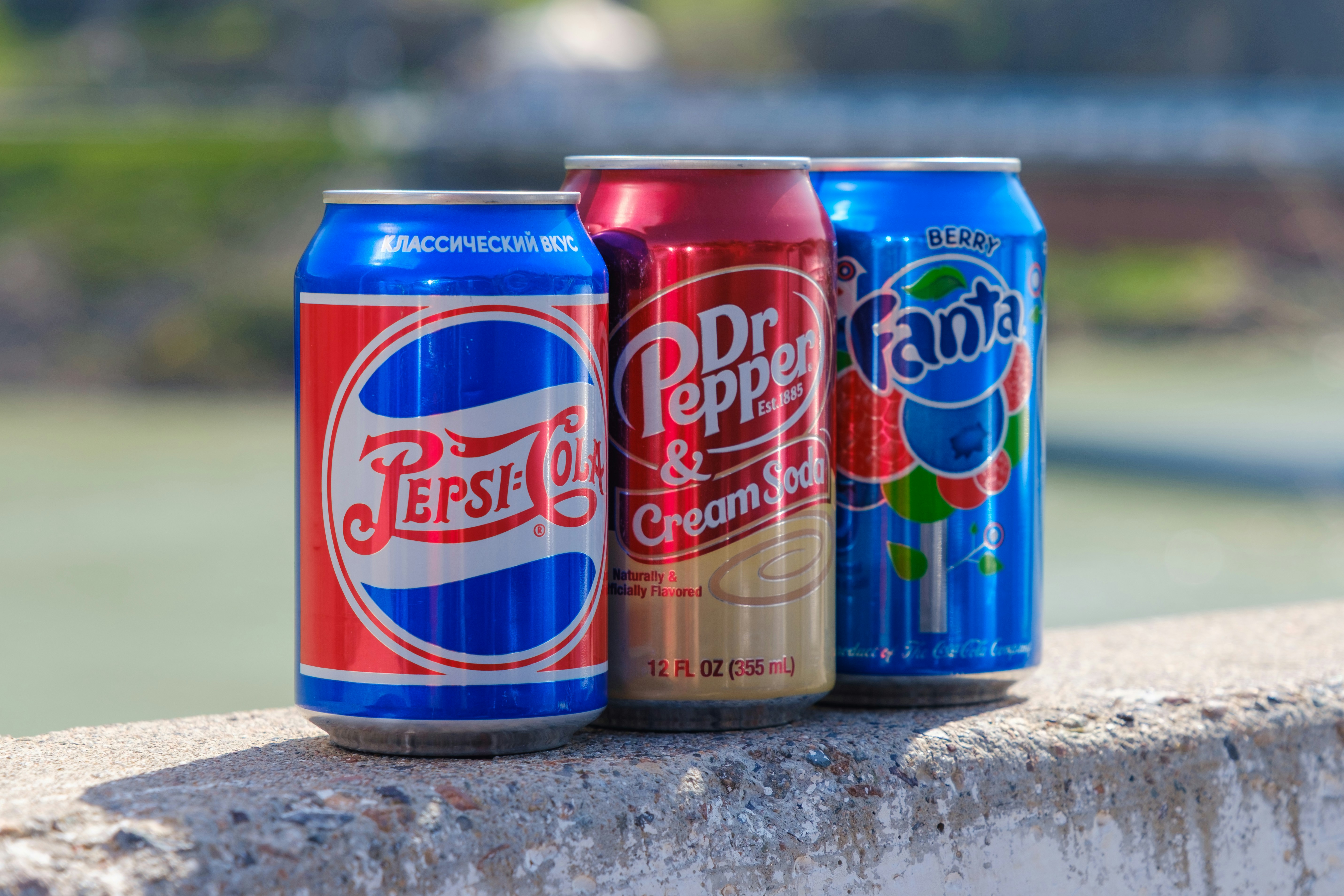 Three Soda Silhouettes: A Trio of Classic Cans on a Sunlit Concrete Edge