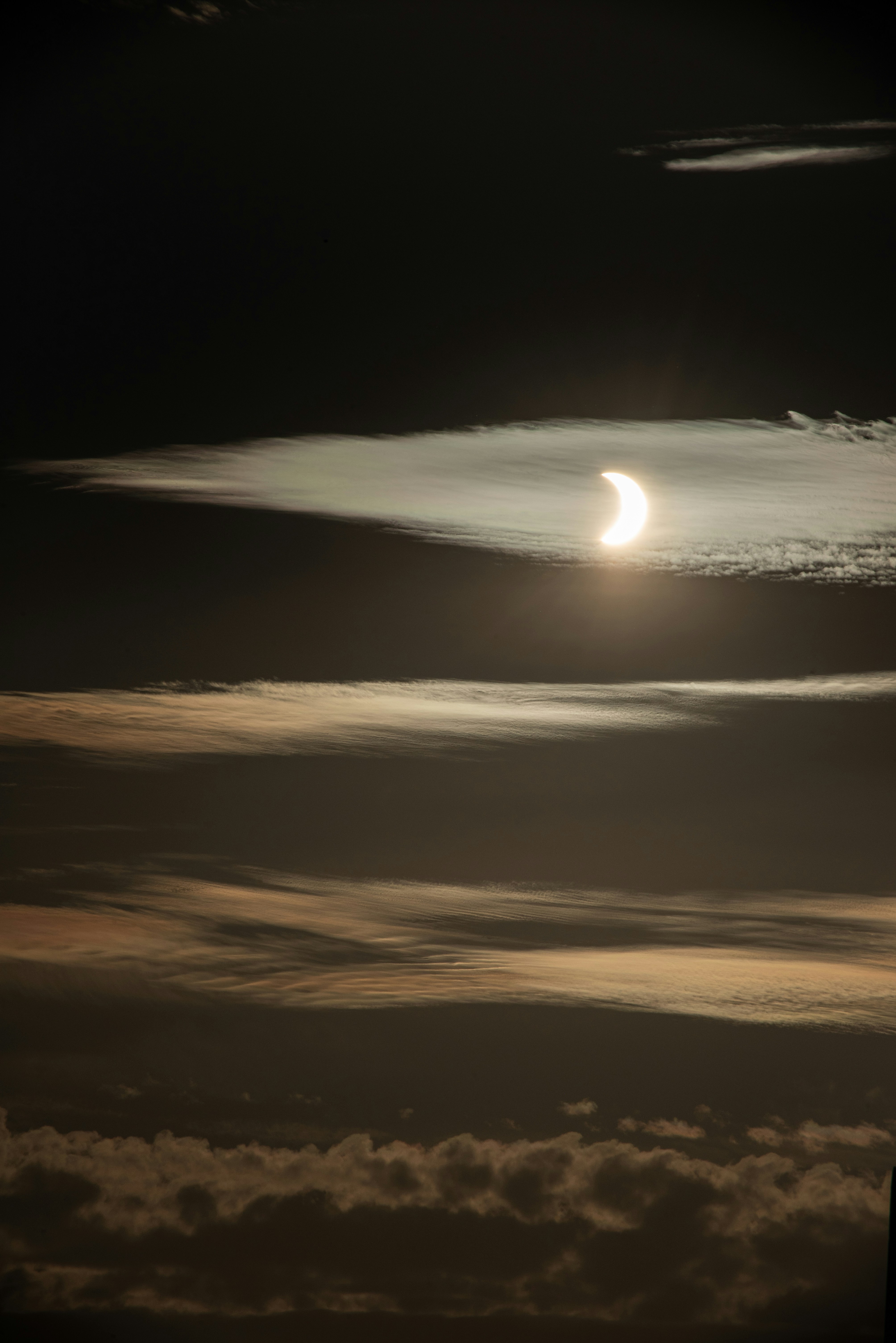 Partial Crescent Moon Above Layered Atmosphere with Subtle Cloud Bands