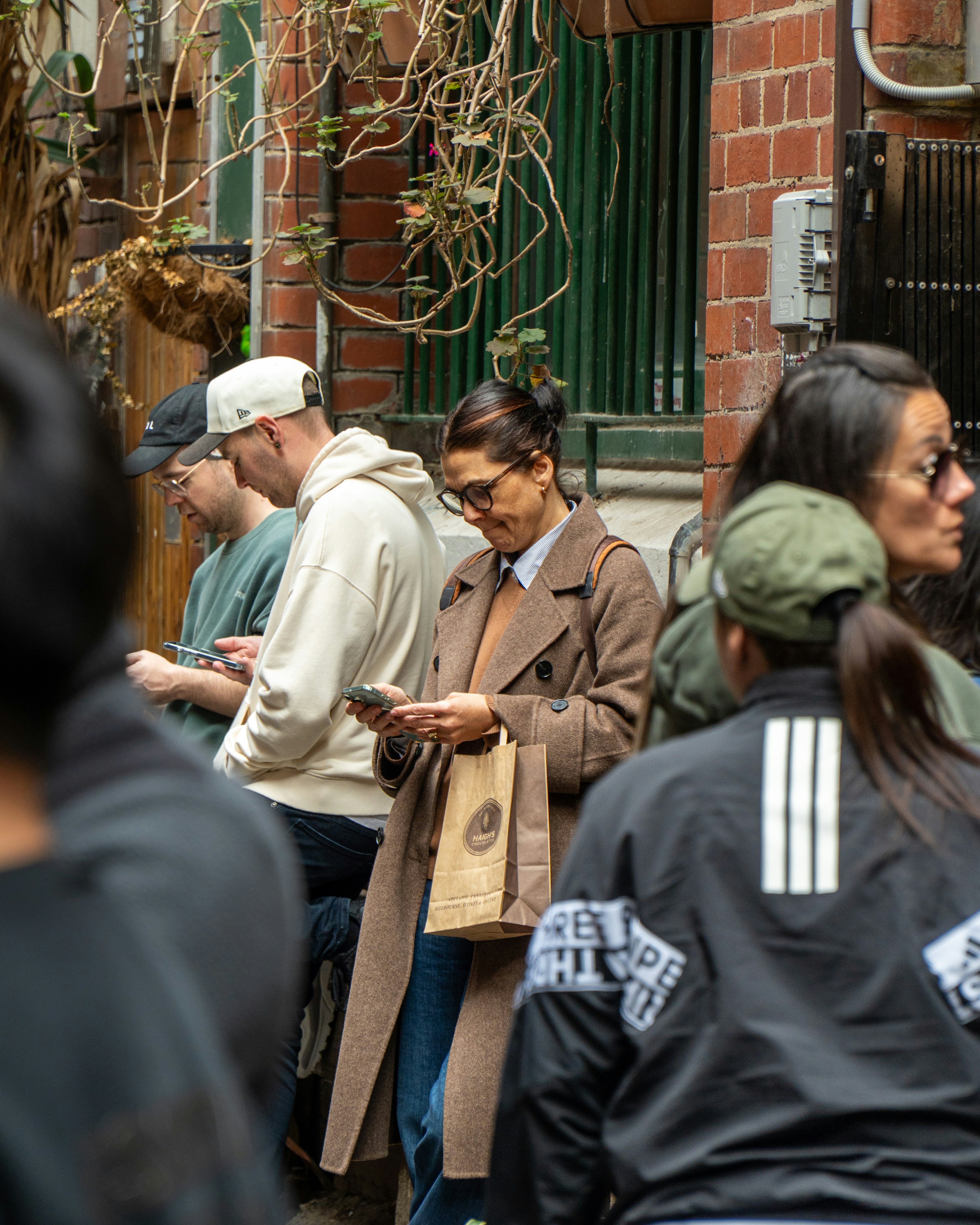 Man in tan coat engrossed in a smartphone amid a city crowd